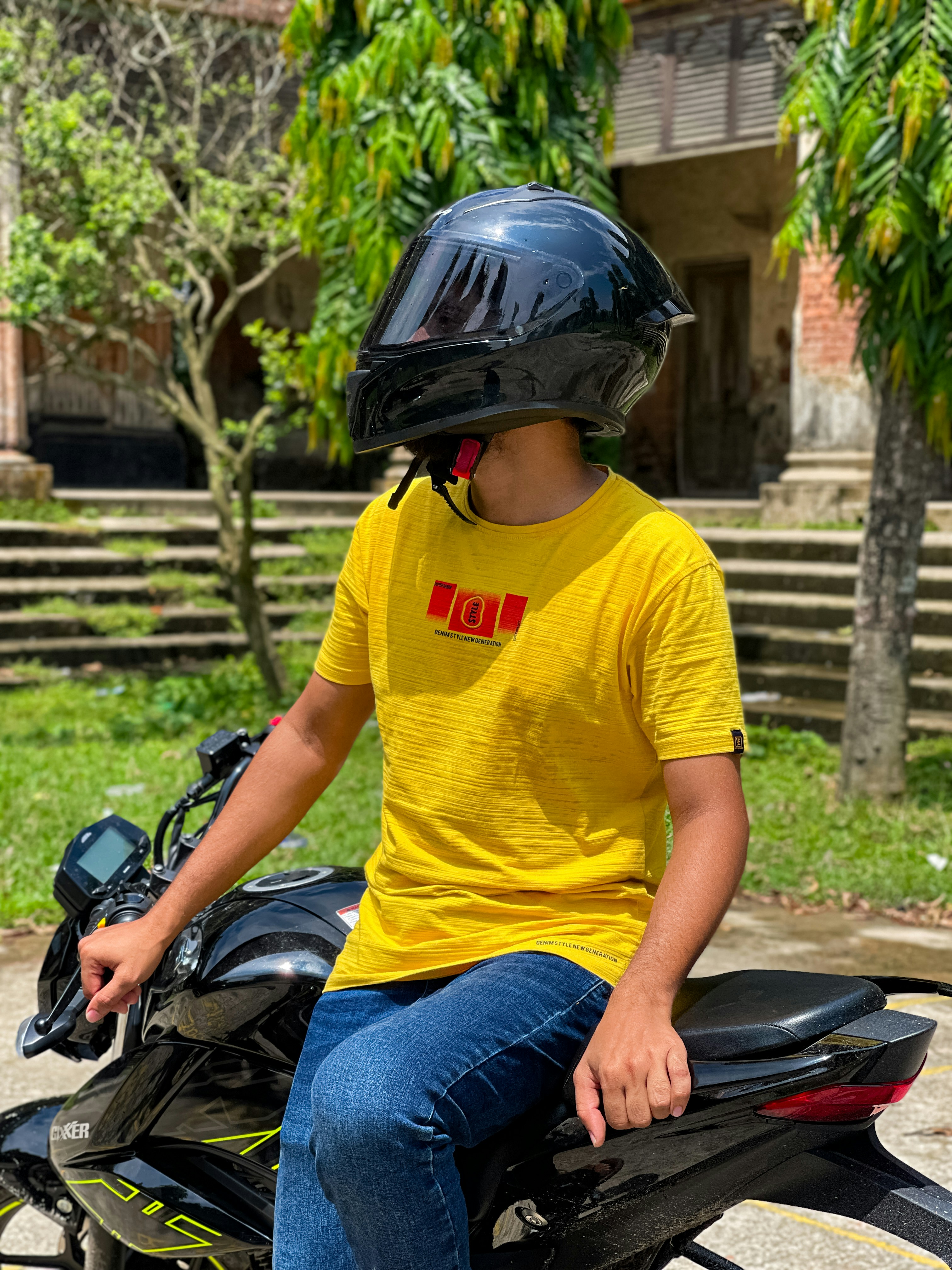 Sunlit Yellow Rider: Quiet Confidence on a Black Motorcycle Amid Greenery
