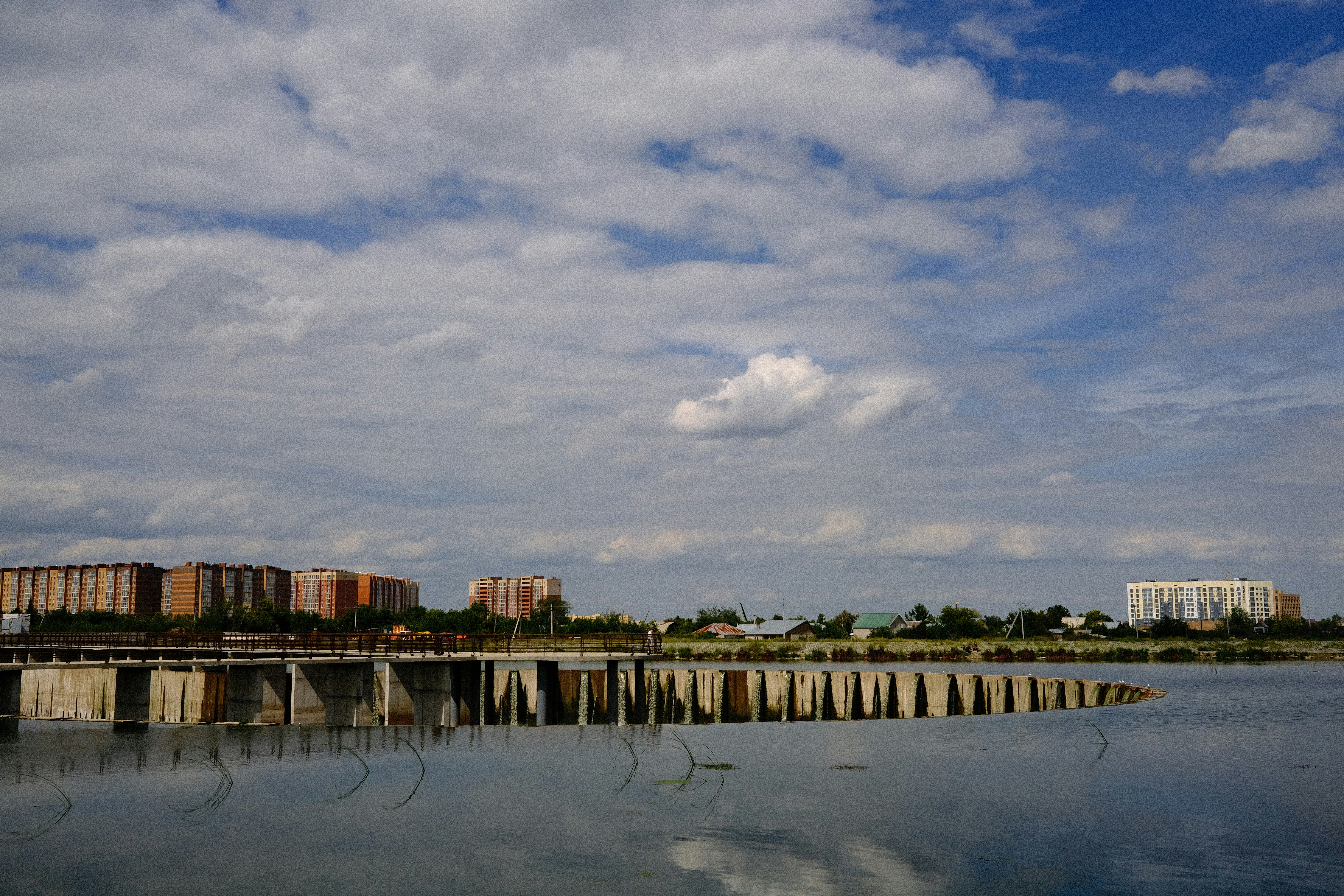 Expansive cityscape with buildings lining a serene waterfront under a partly cloudy sky.