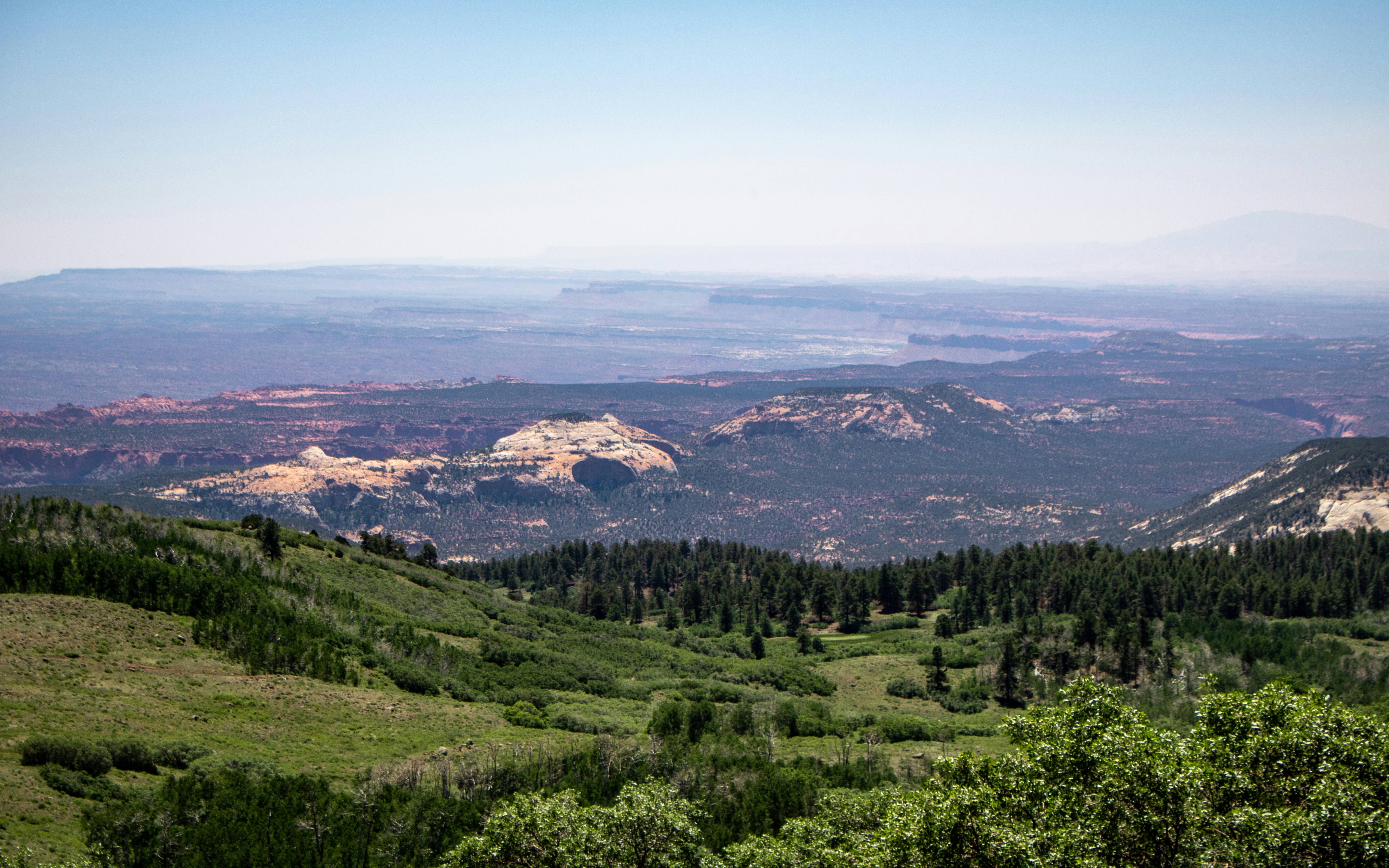 Expansive landscape with lush green valleys and distant rugged hills under a clear blue sky.