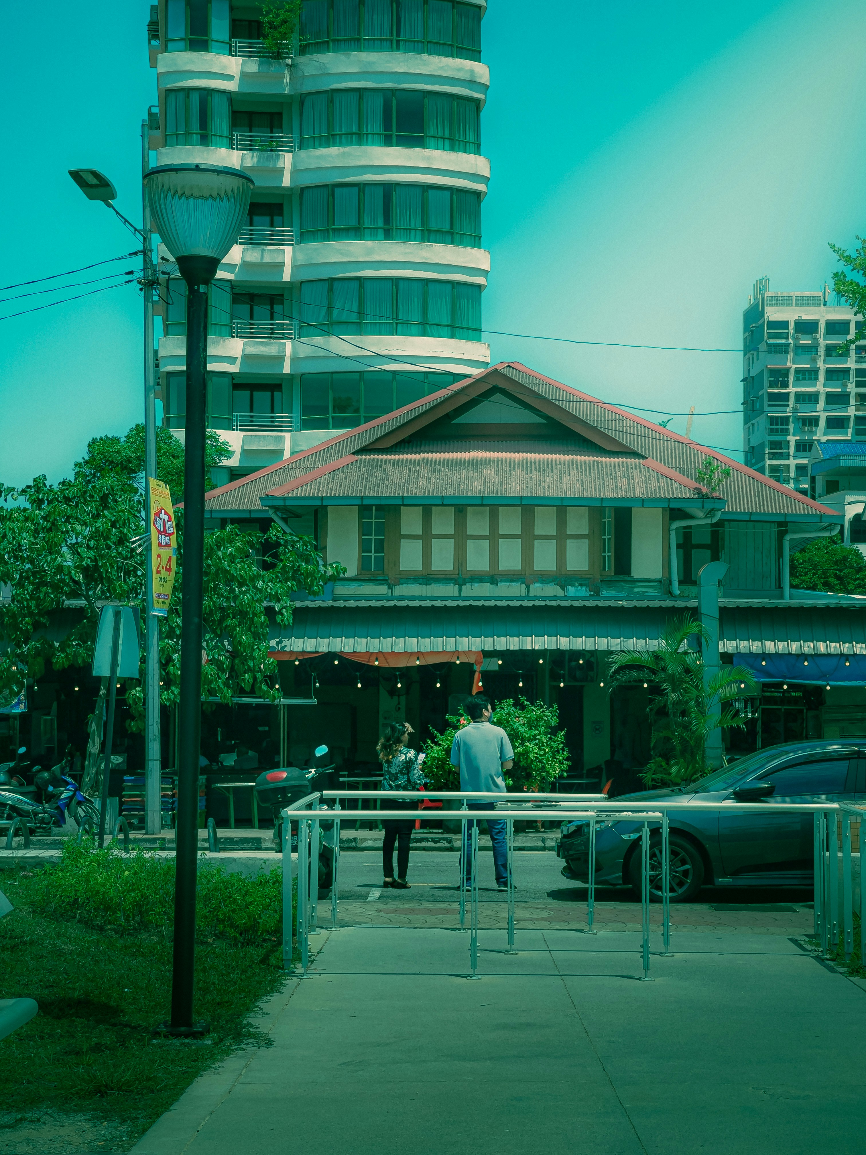 Teal-Flooded Street: Café Fronts a Curved-Glass Tower