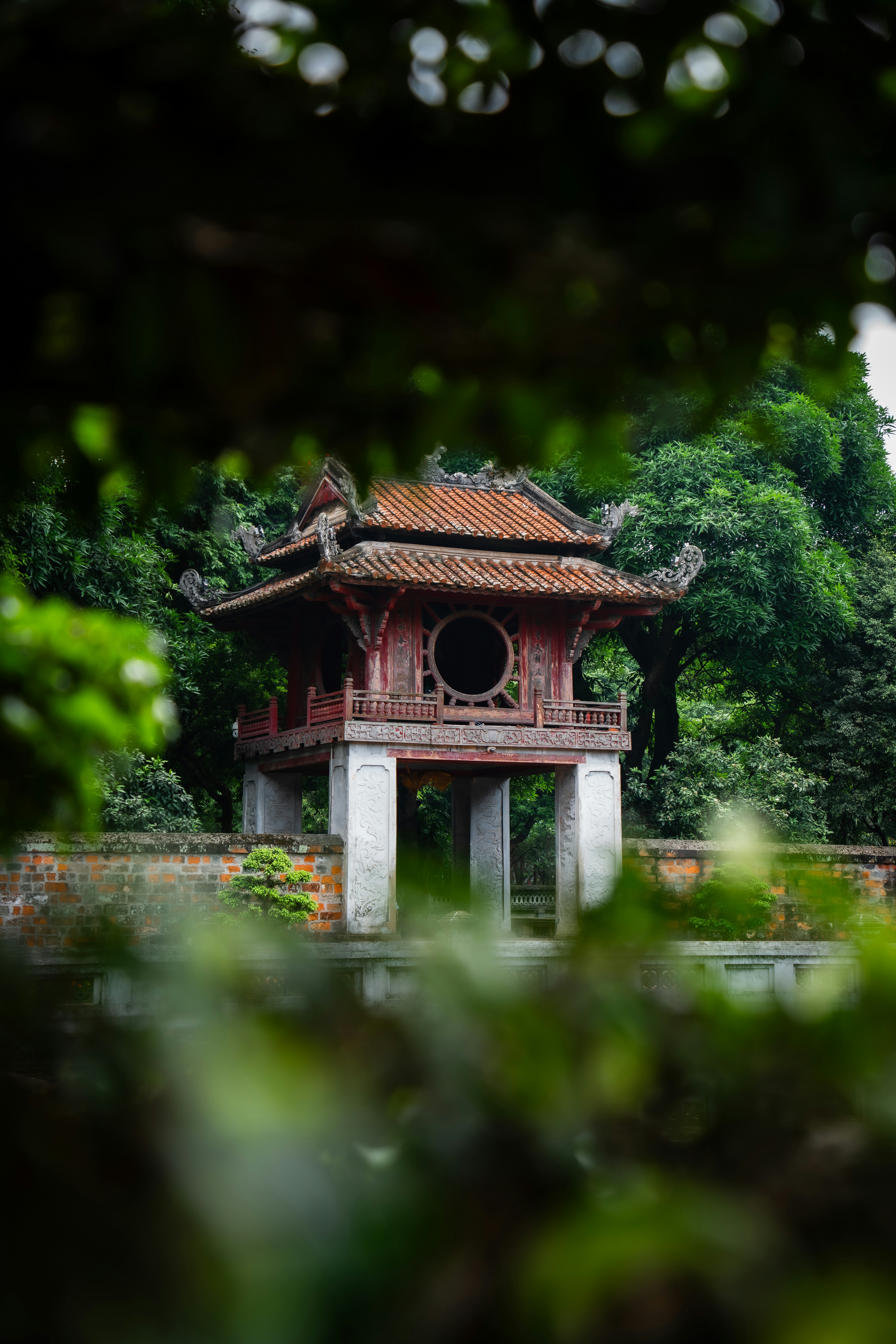 A traditional pavilion framed by lush greenery, showcasing intricate architecture and historical significance. The structure's circular window offers a glimpse into cultural heritage.