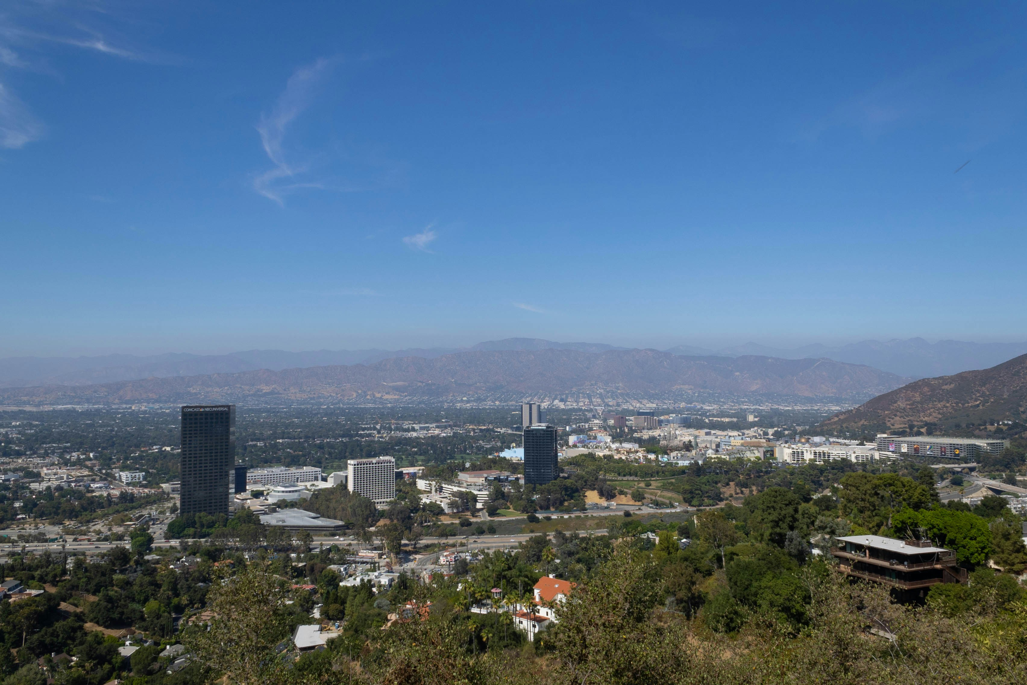 A panoramic view of a sprawling cityscape framed by distant mountains under a clear blue sky.