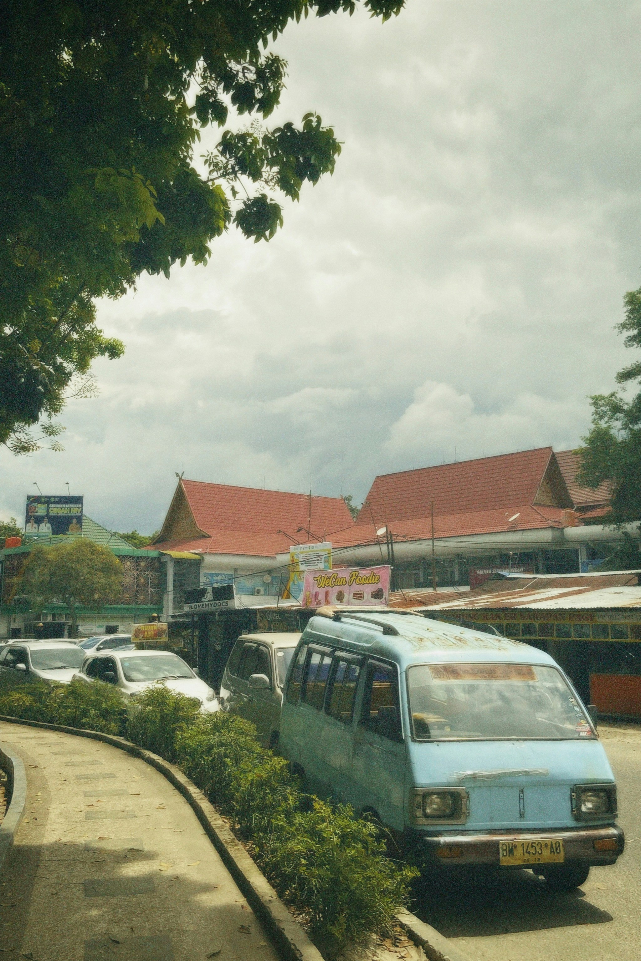 Blue Minibus at a Curved Market Lane Beneath an Overcast Sky