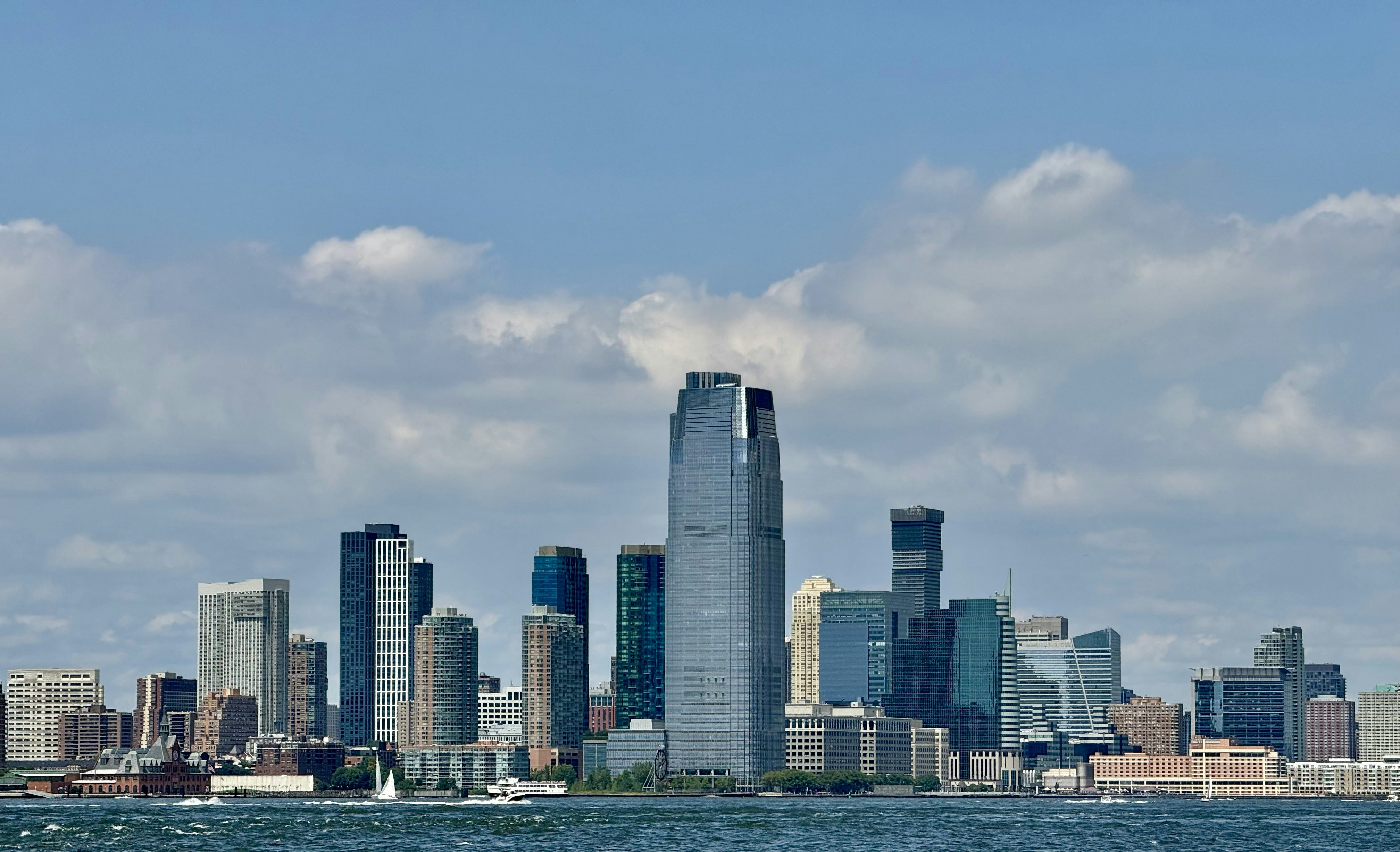 A vibrant city skyline with modern skyscrapers reflecting in the water under a partly cloudy sky.