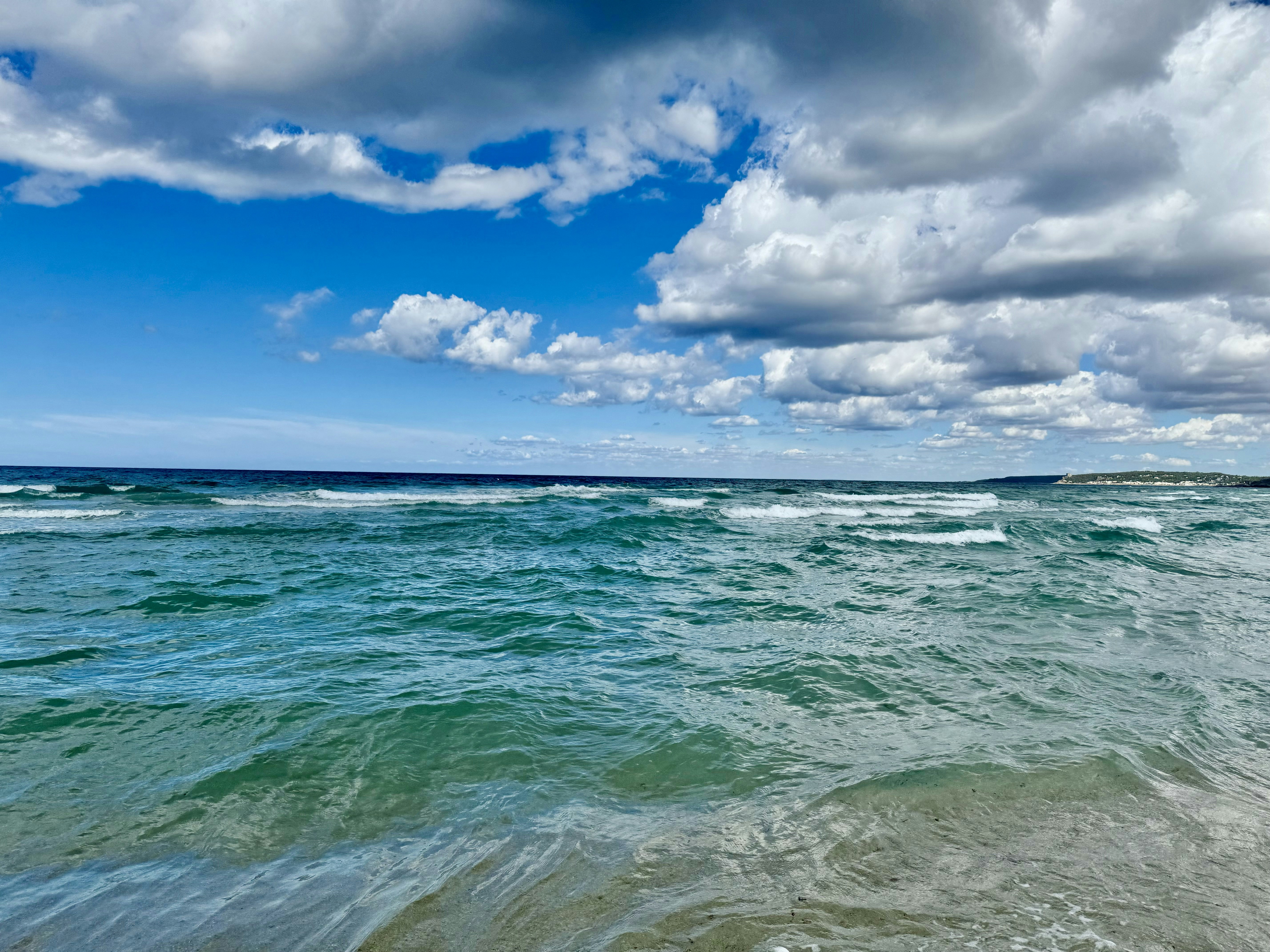 Vibrant ocean waters meet the horizon beneath a sky filled with dynamic clouds.
