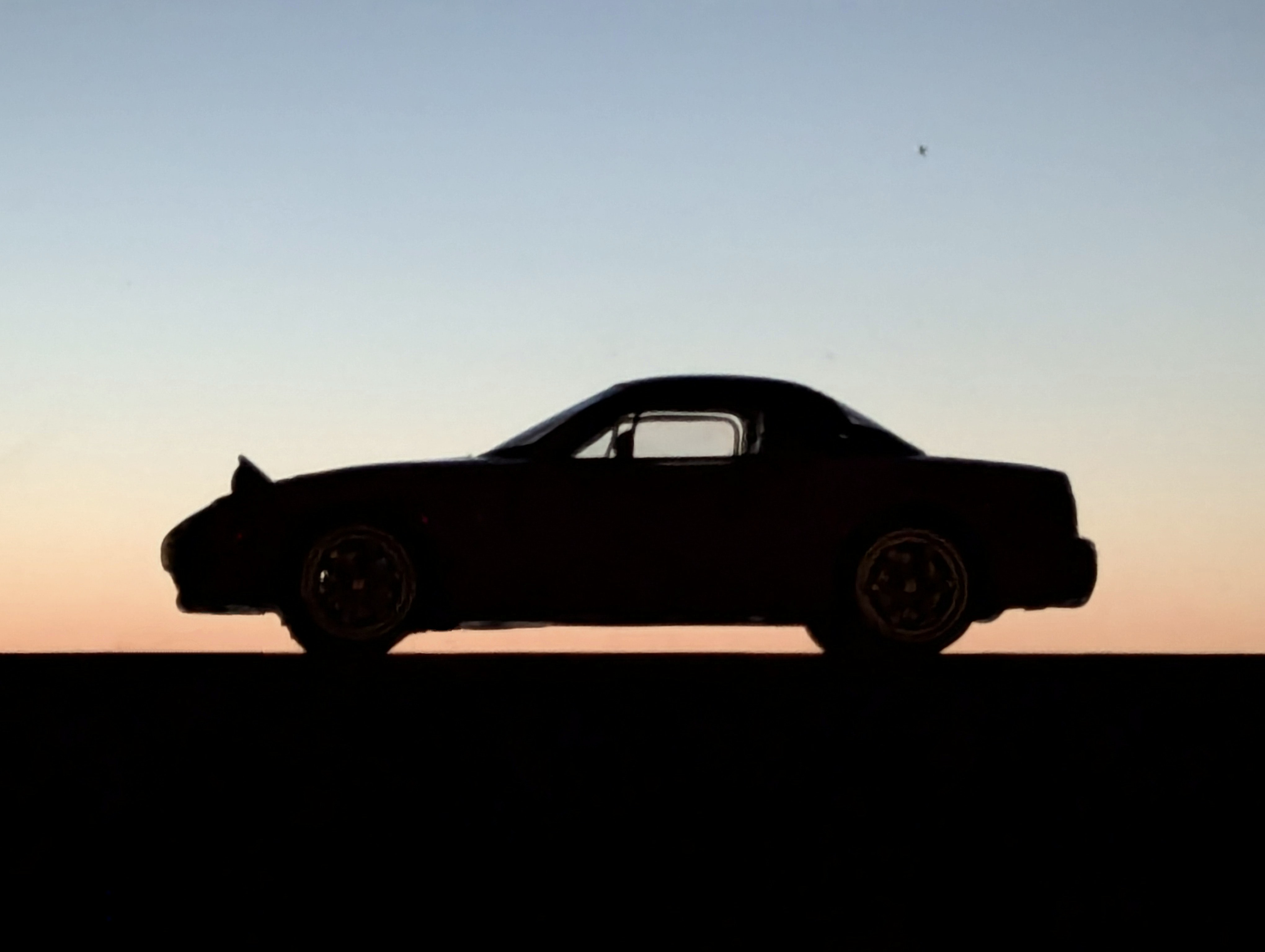 Silhouette of a classic coupe on a flat horizon at sunset. The gradient sky shifts from warm orange to cool blue behind the profile.