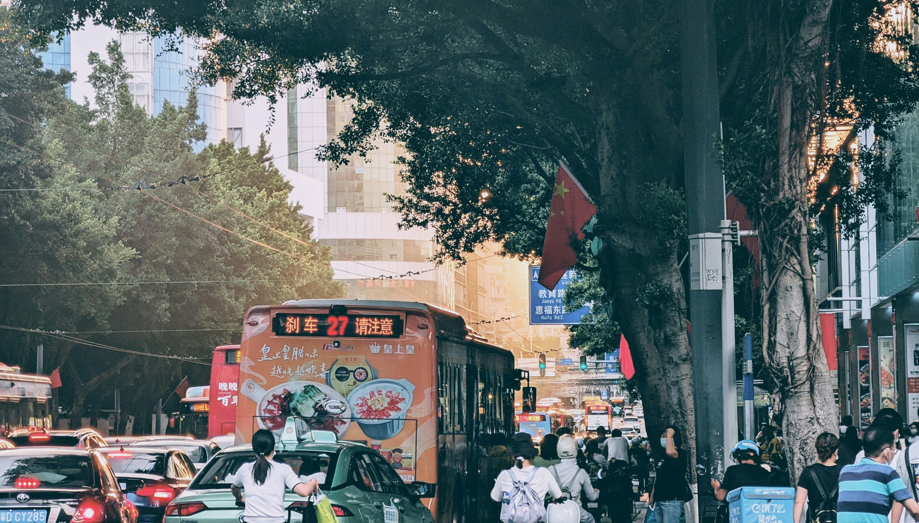Bustling city street with heavy traffic under a canopy of trees and urban skyscrapers.