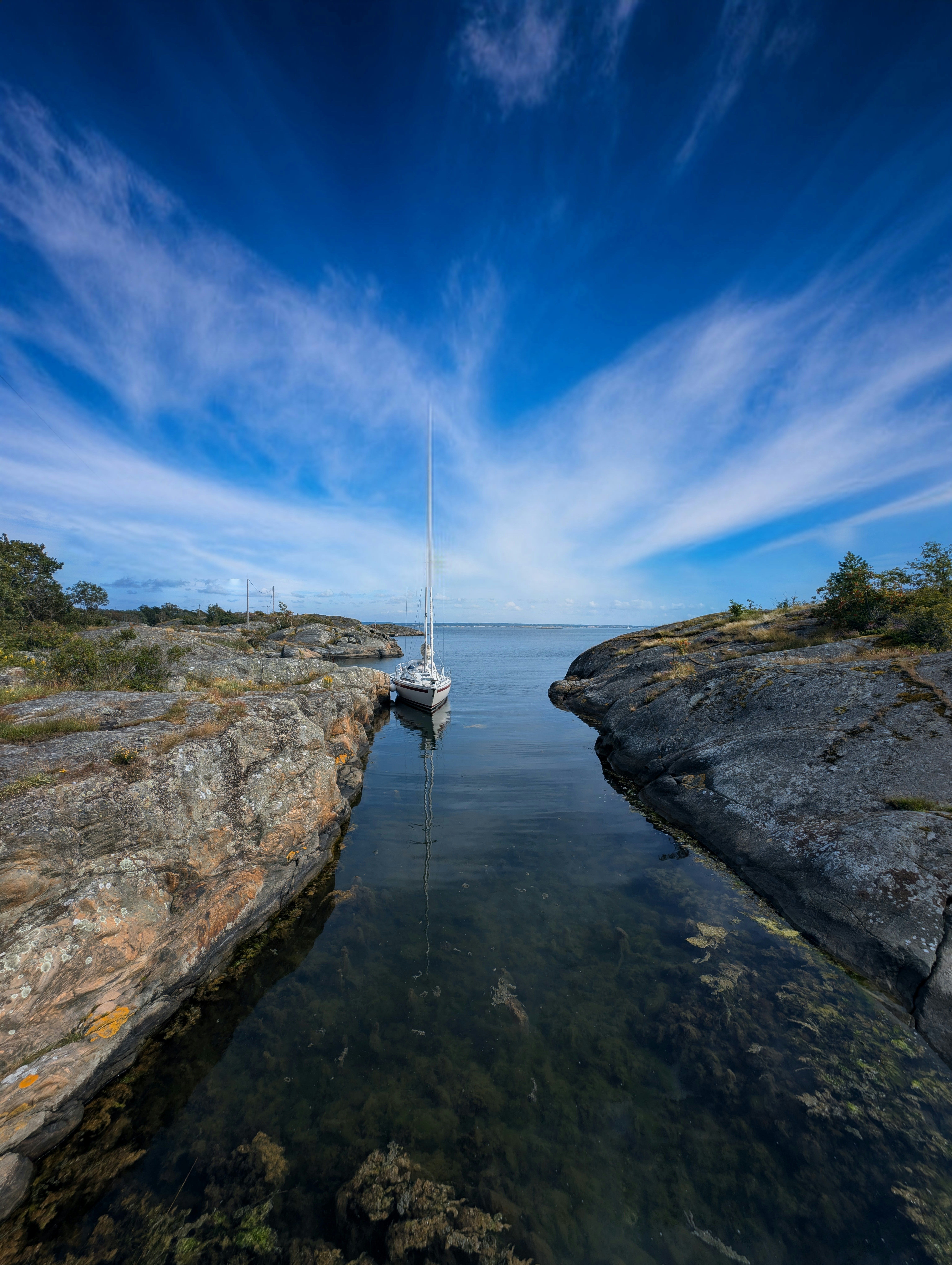 Lone sailboat rests in a narrow channel between rocky shores beneath a vast blue sky.