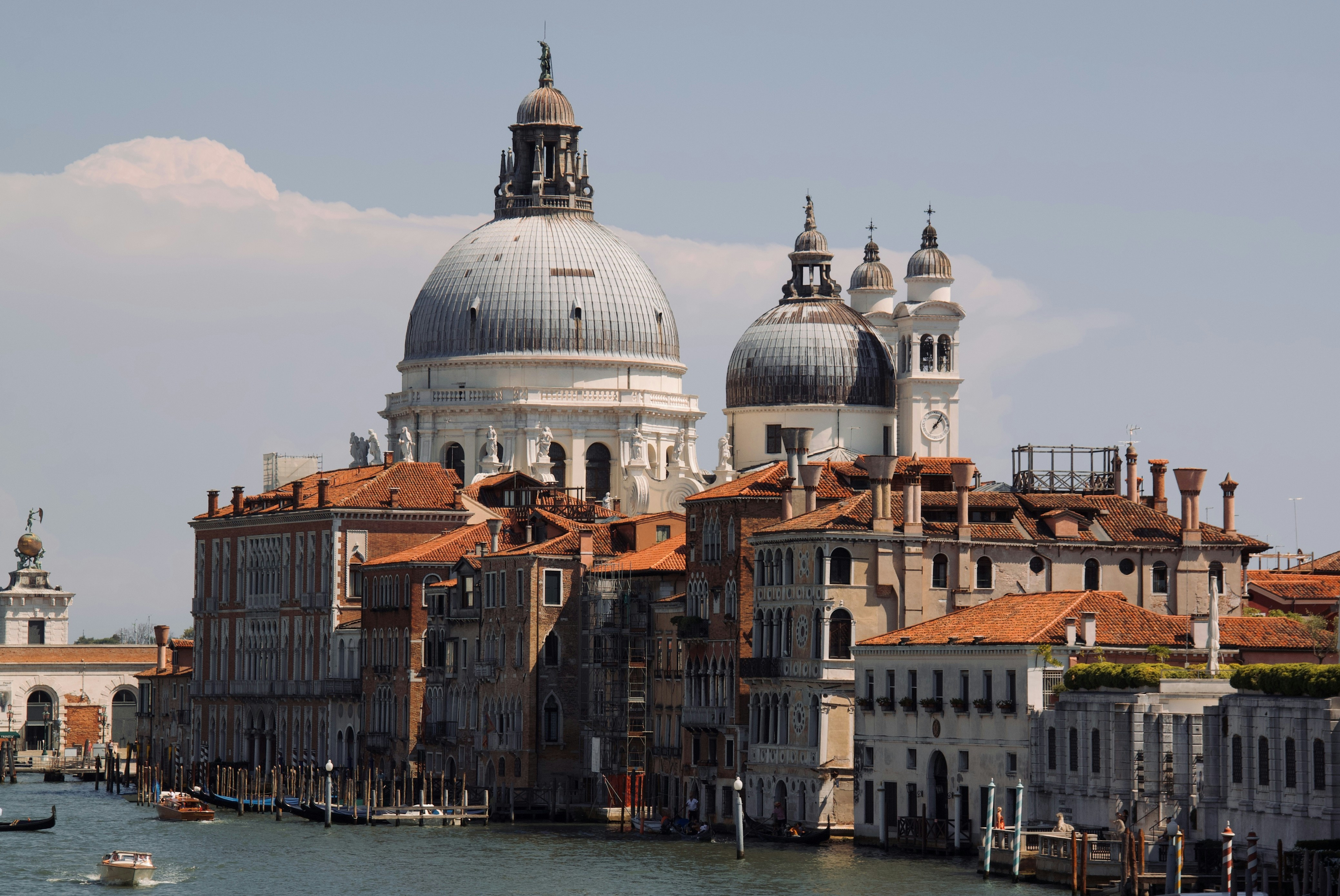 Historic Venetian buildings with domes and red rooftops along a canal under a clear sky.