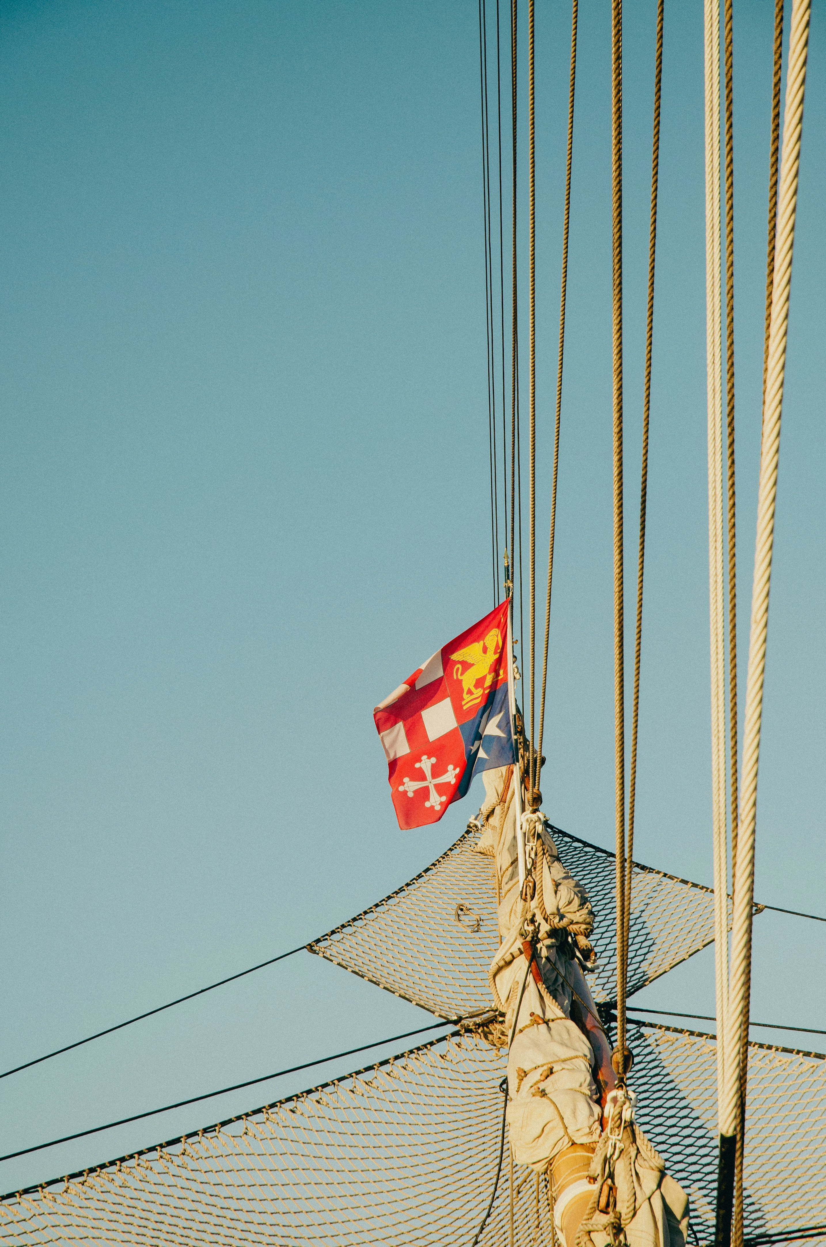 Flags at the Crown: Red-and-Gold Emblems Rising Above the Ship's Rigging
