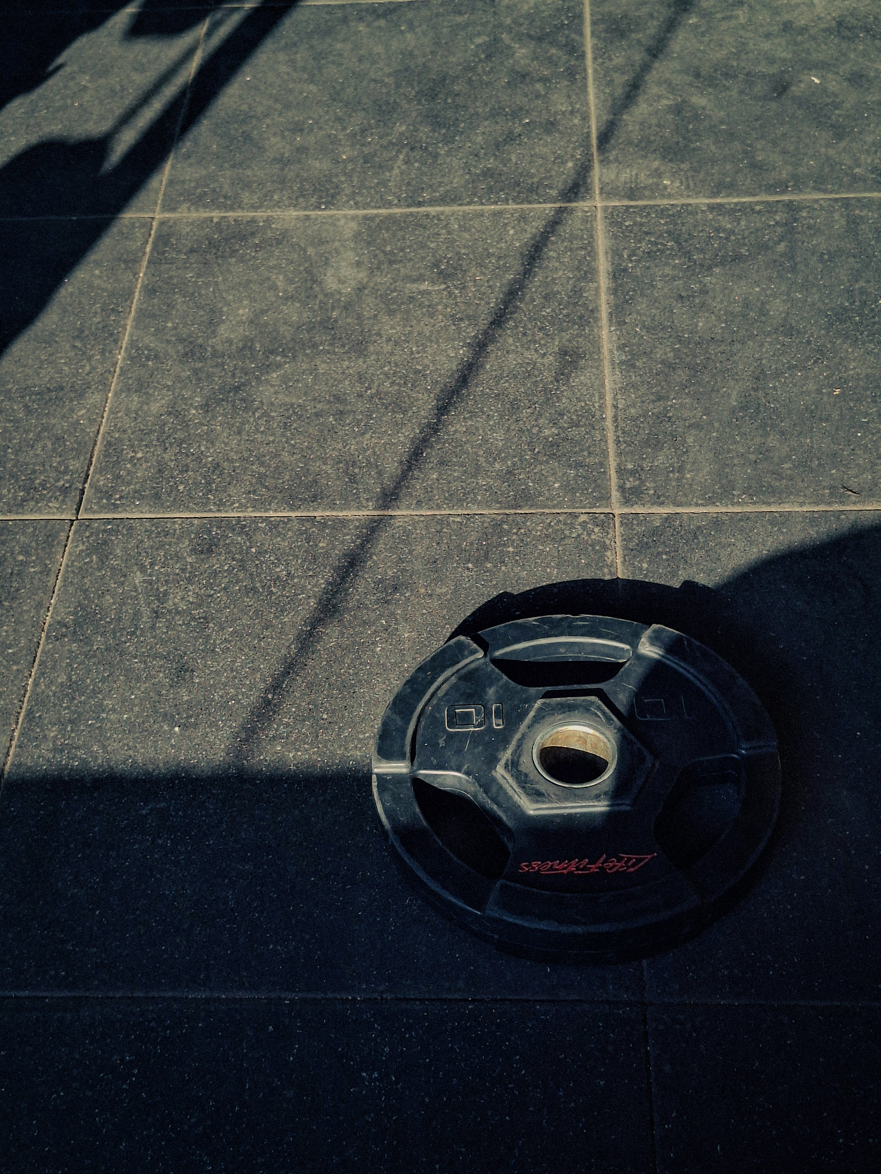 A solitary weight plate rests on dark tiles, partially obscured by shadows that create a dramatic contrast.