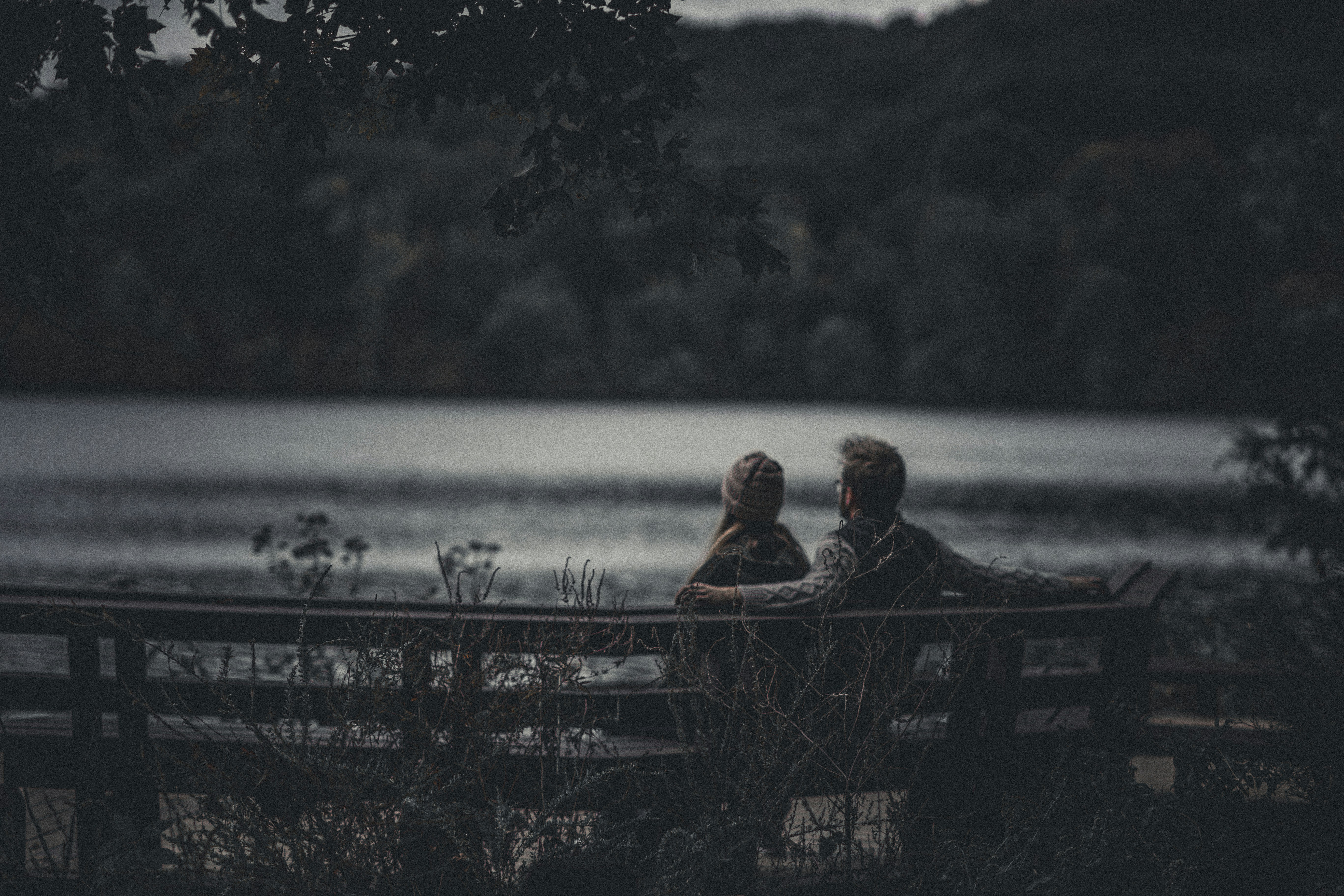 Couple sitting on a bench overlooking a serene lake, surrounded by autumn foliage. The scene evokes a sense of tranquility and connection.