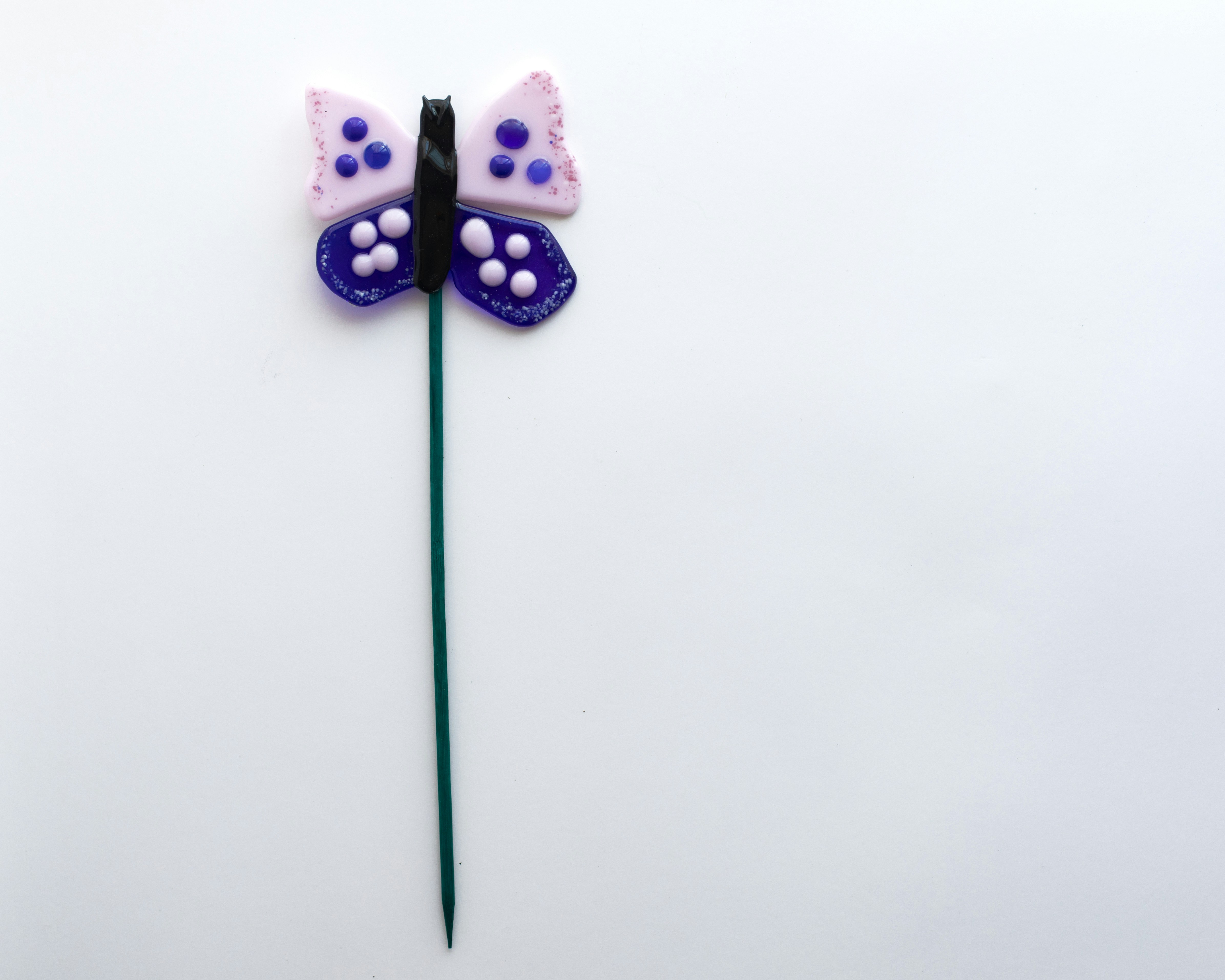 Purple-winged butterfly pin on a slender green stake against a stark white background