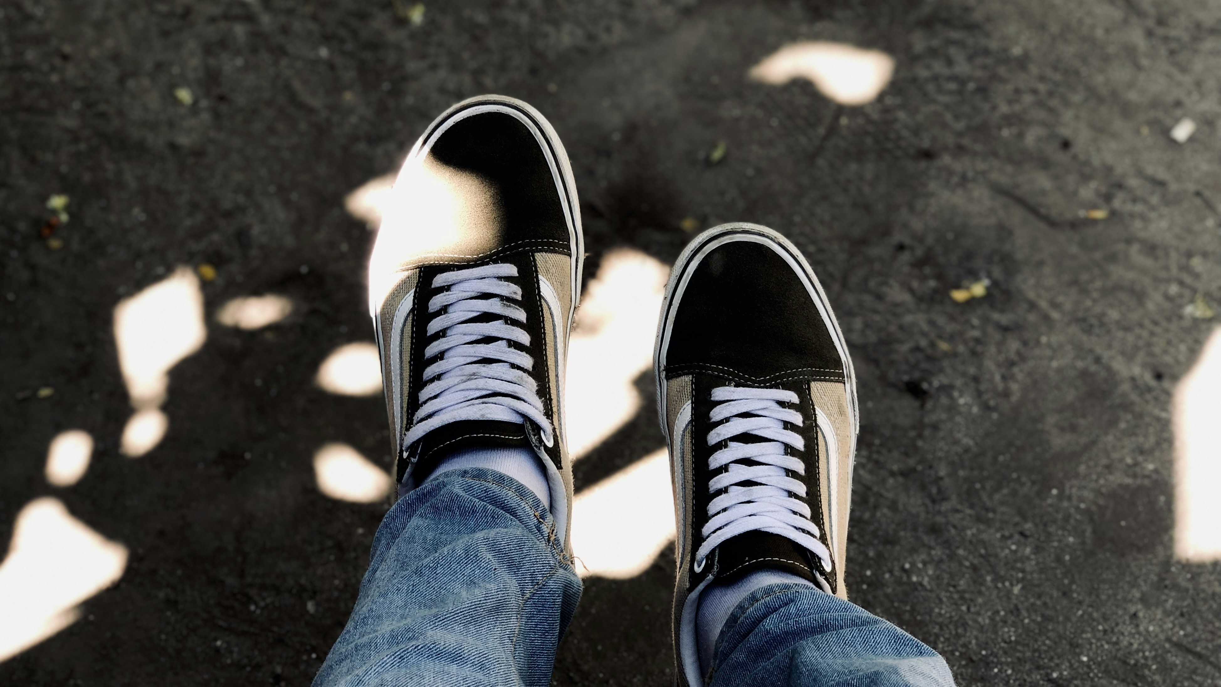 Casual sneakers resting on a textured surface, highlighted by playful shadows from overhead foliage.