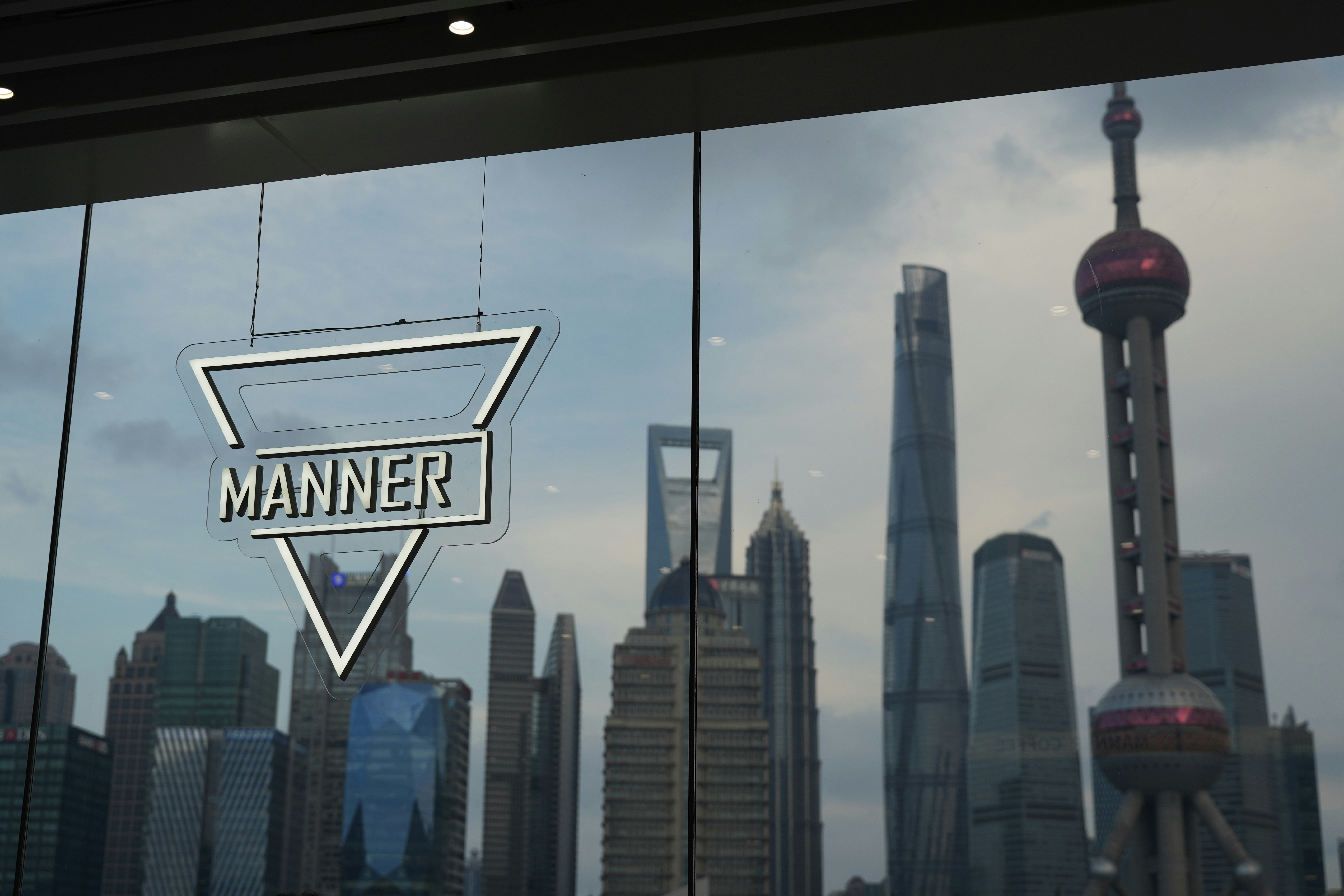 MANNER Triangle Logo Framed by a Glass-Washed Urban Silhouette