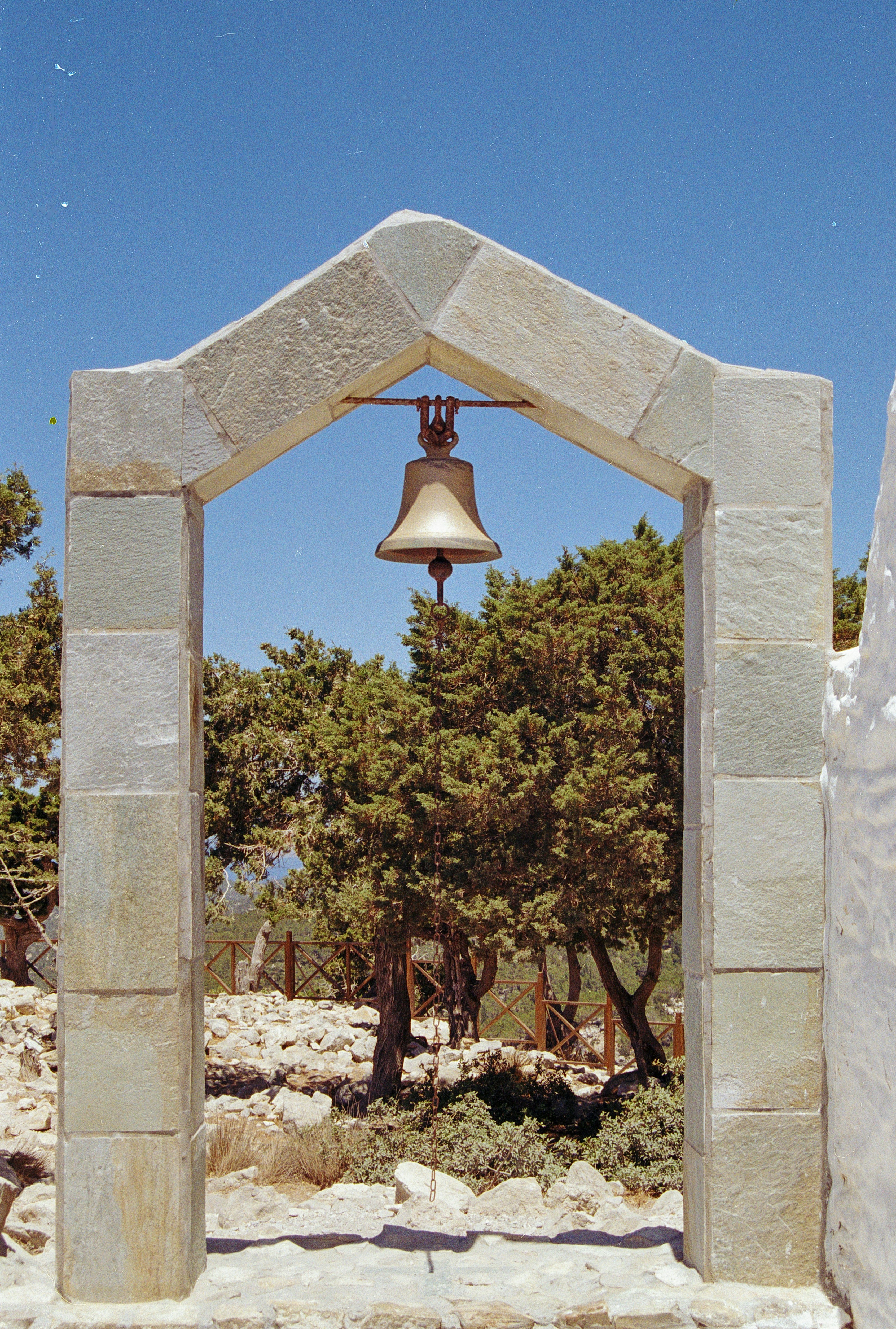 Bell beneath a Stone Archway: Sunlit Courtyard Framed by Evergreen Backdrop