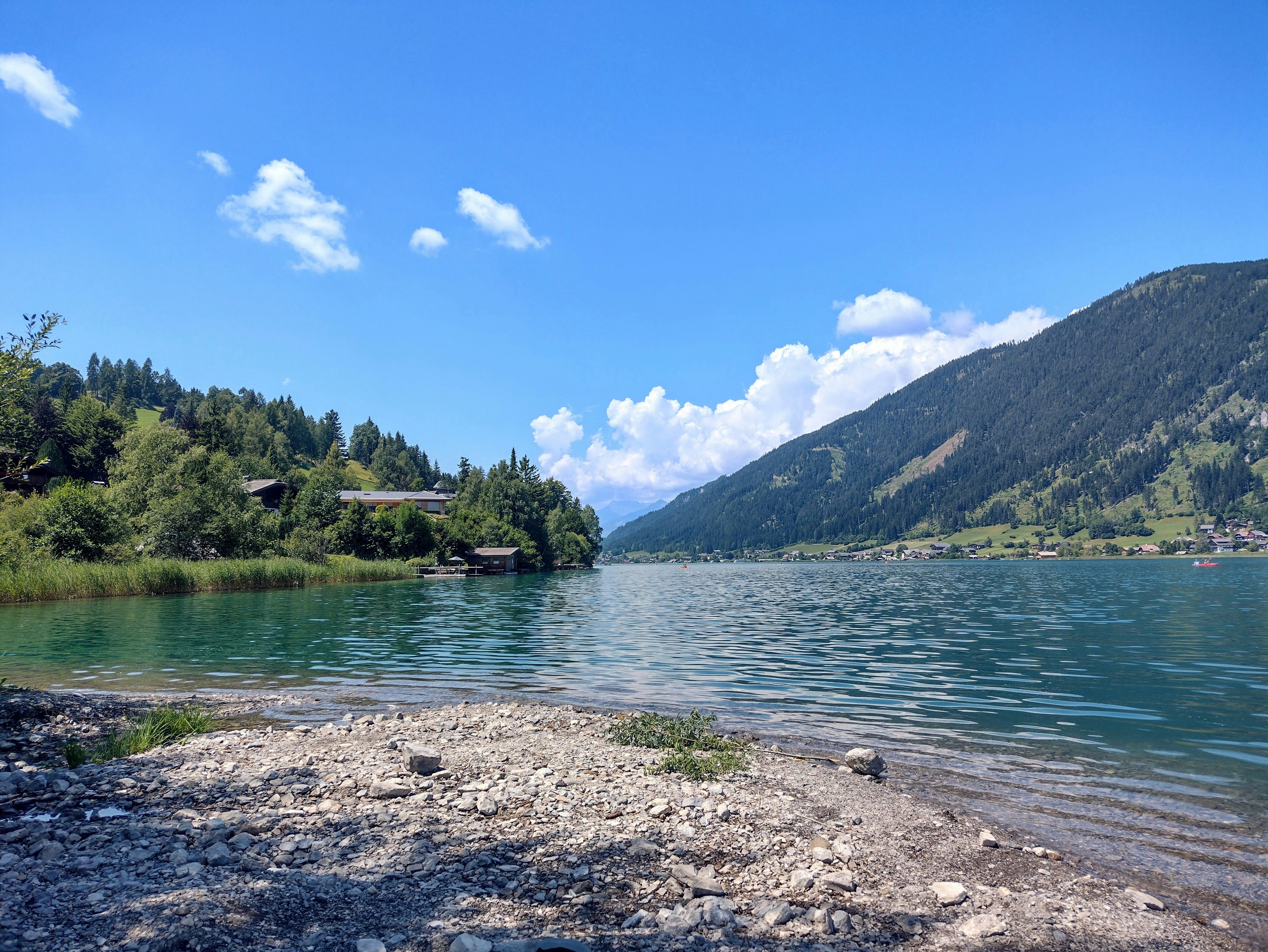Serene lake bordered by lush greenery and towering mountains under a clear blue sky.