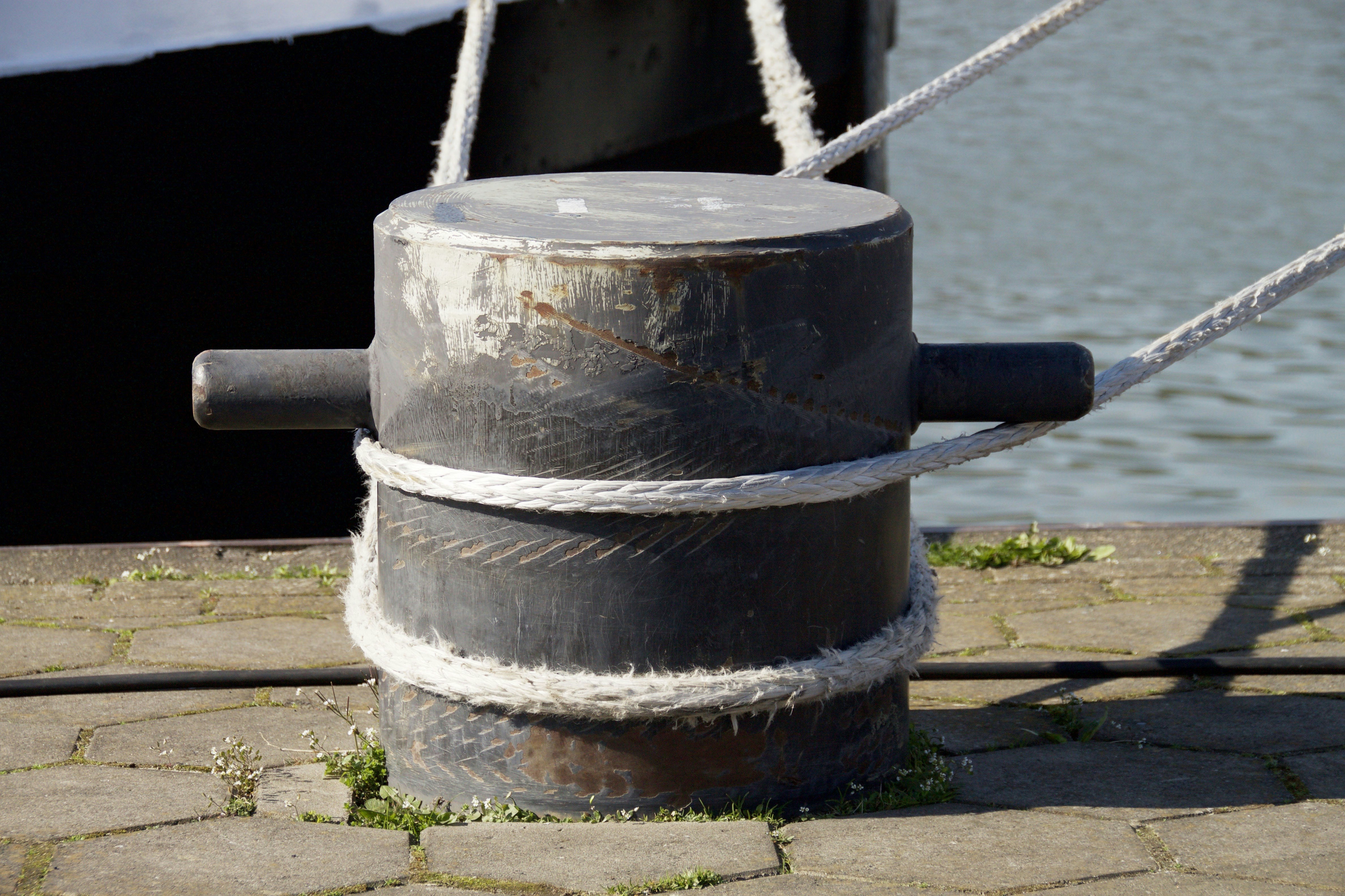 Roped Sentinel: A Weathered Dock Bollard Bound by White Lines