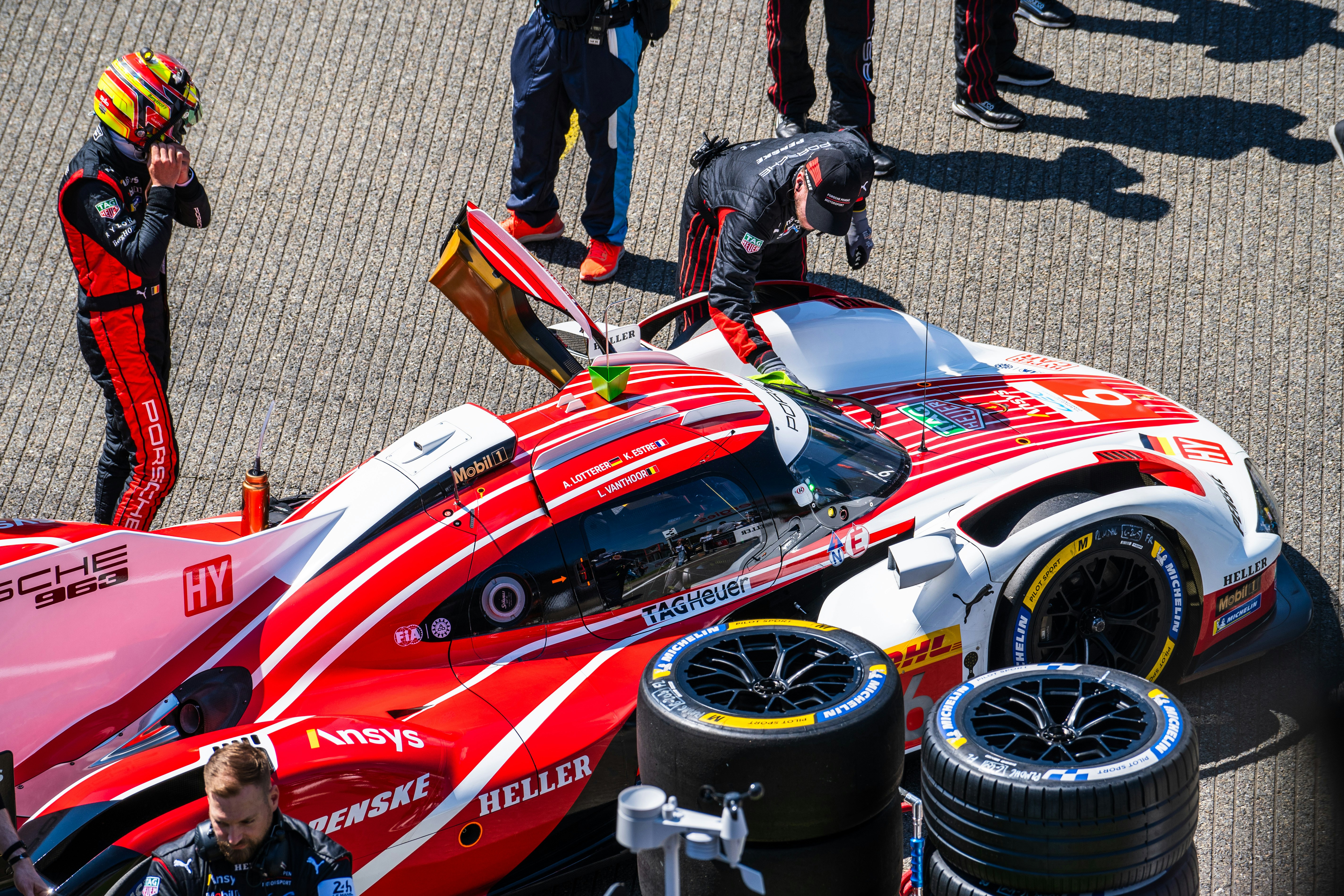 Race car with red and white livery being serviced by crew in a pit stop, surrounded by spare tires and team members.