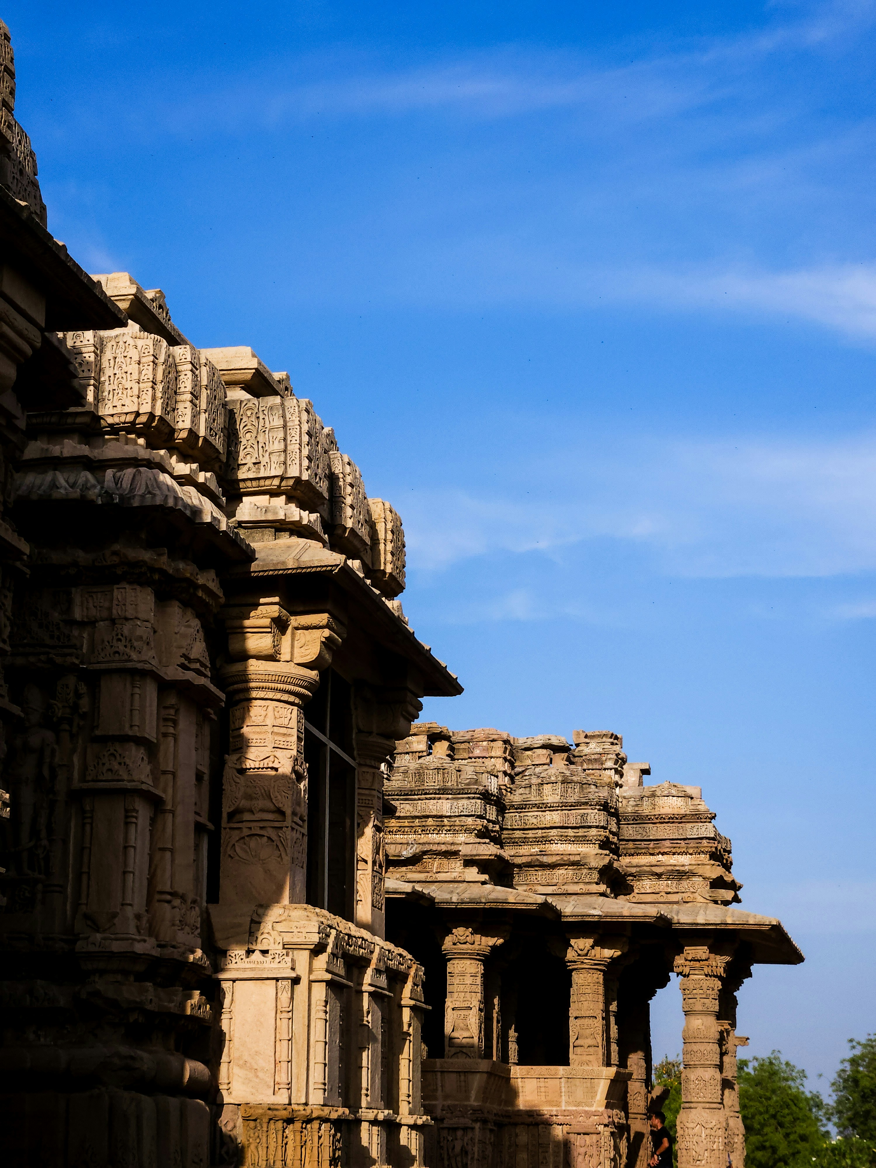 Ornate sandstone temple ruins rise along the left, revealing intricate carvings and stacked columns. The clear blue sky contrasts with the weathered texture, underscoring the architecture's timeless detail.