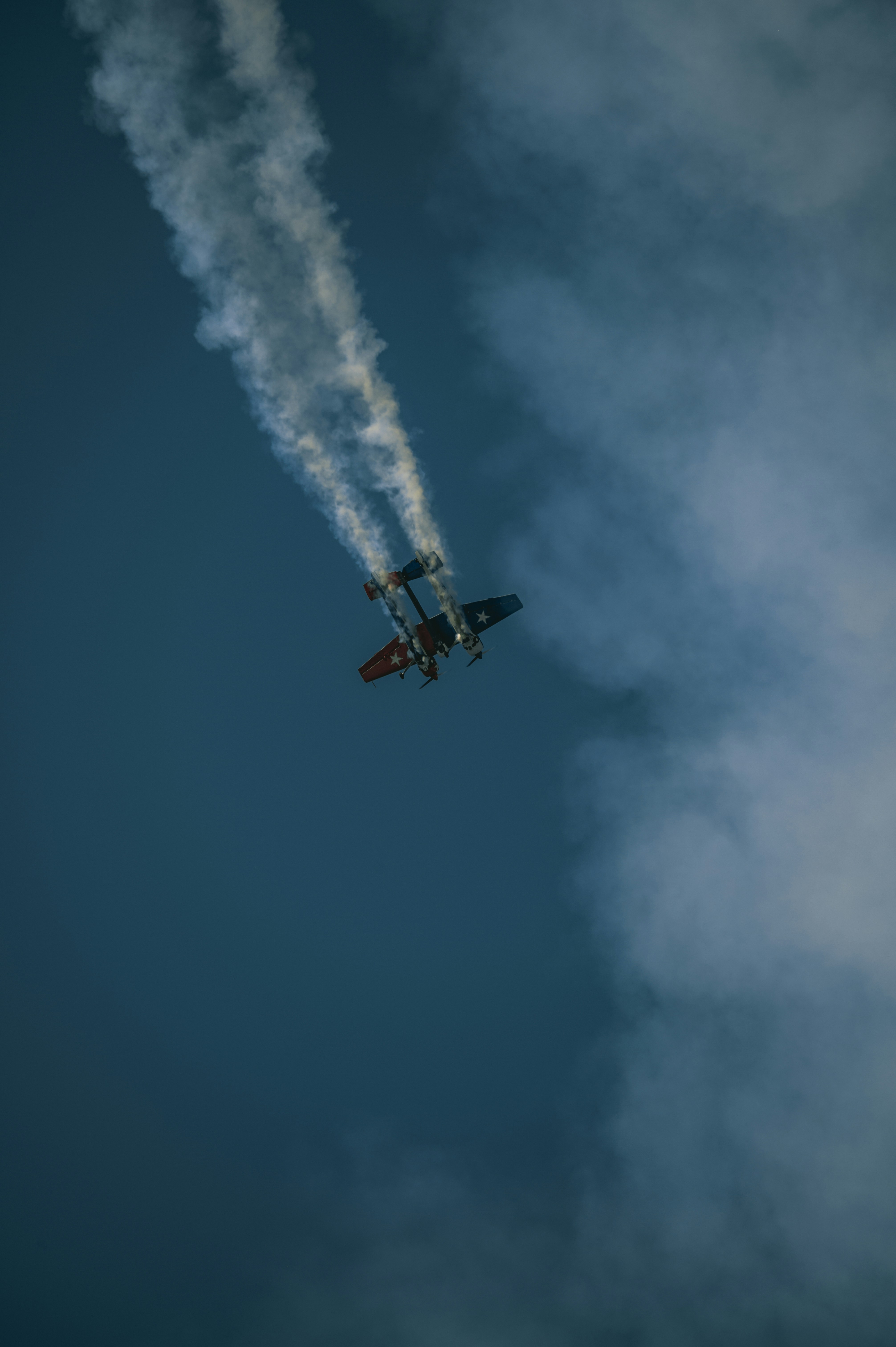 Blue Descent: A Vintage Aerobatic Plane Traces Smoke Across the Sky