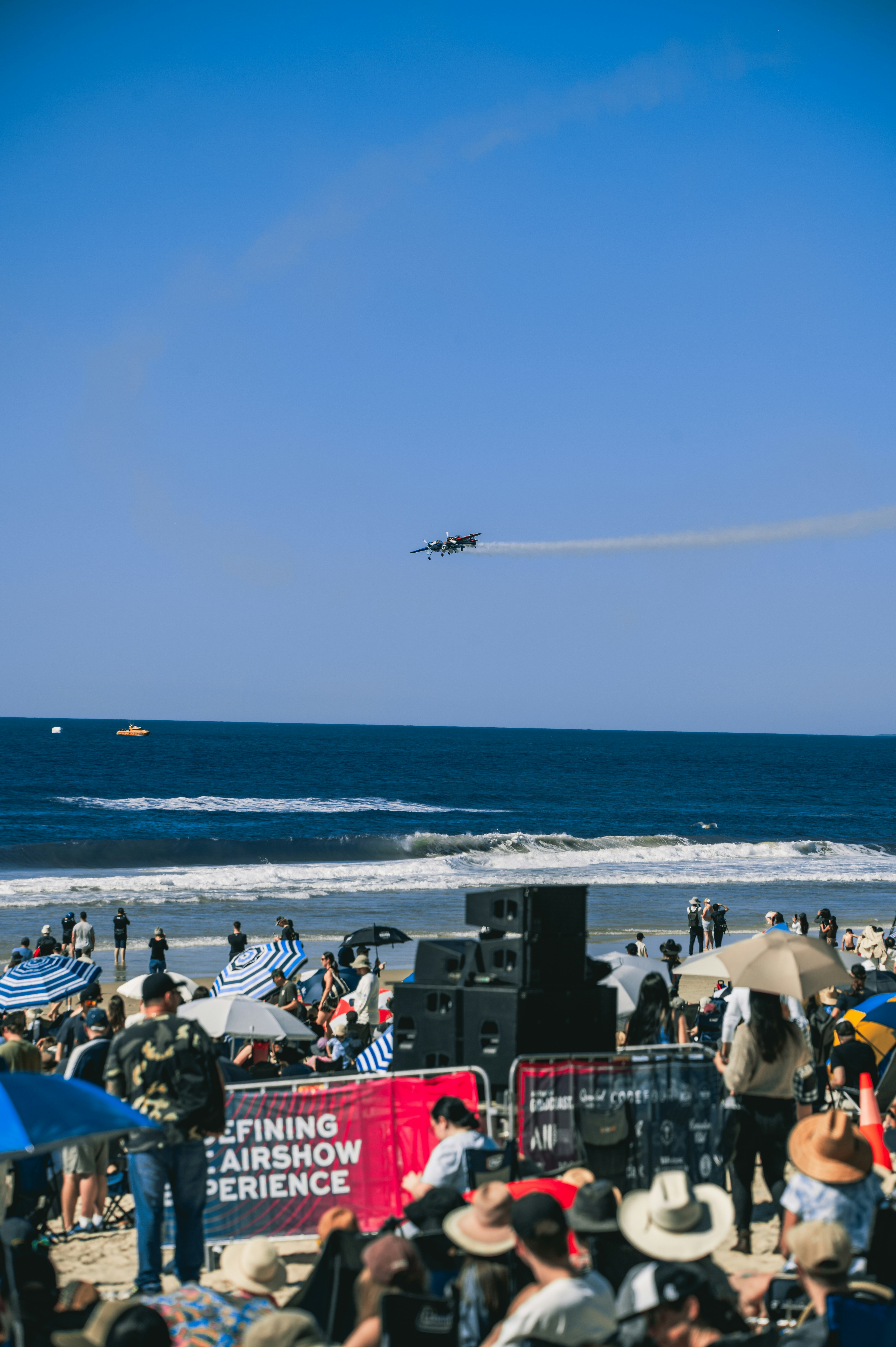 Airshow Over a Crowded Beach: A Plane's Thin White Wake Across a Blue Horizon