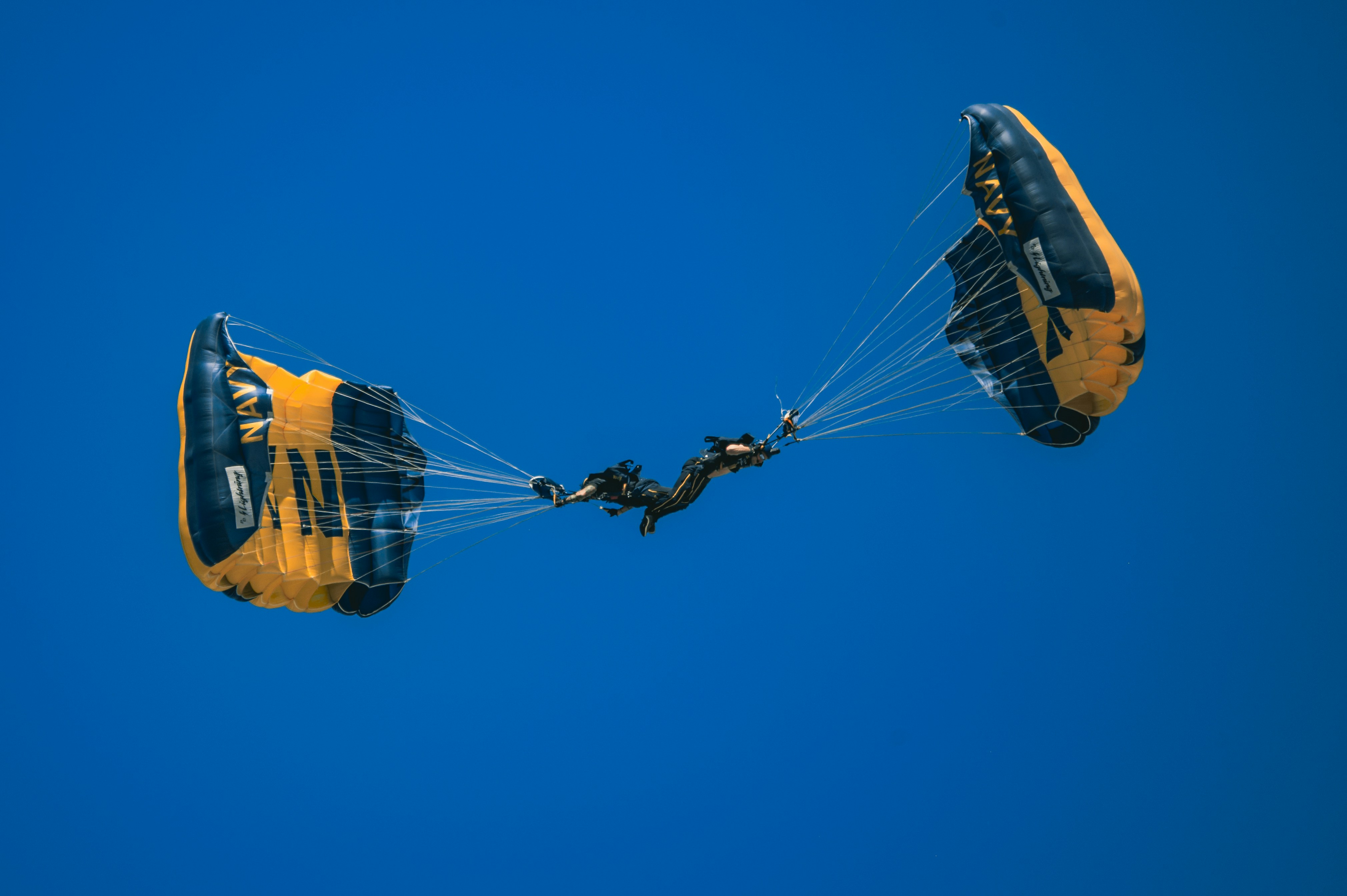 Midair Confluence: Skydiver Between Twin Canopies in a Cobalt Sky