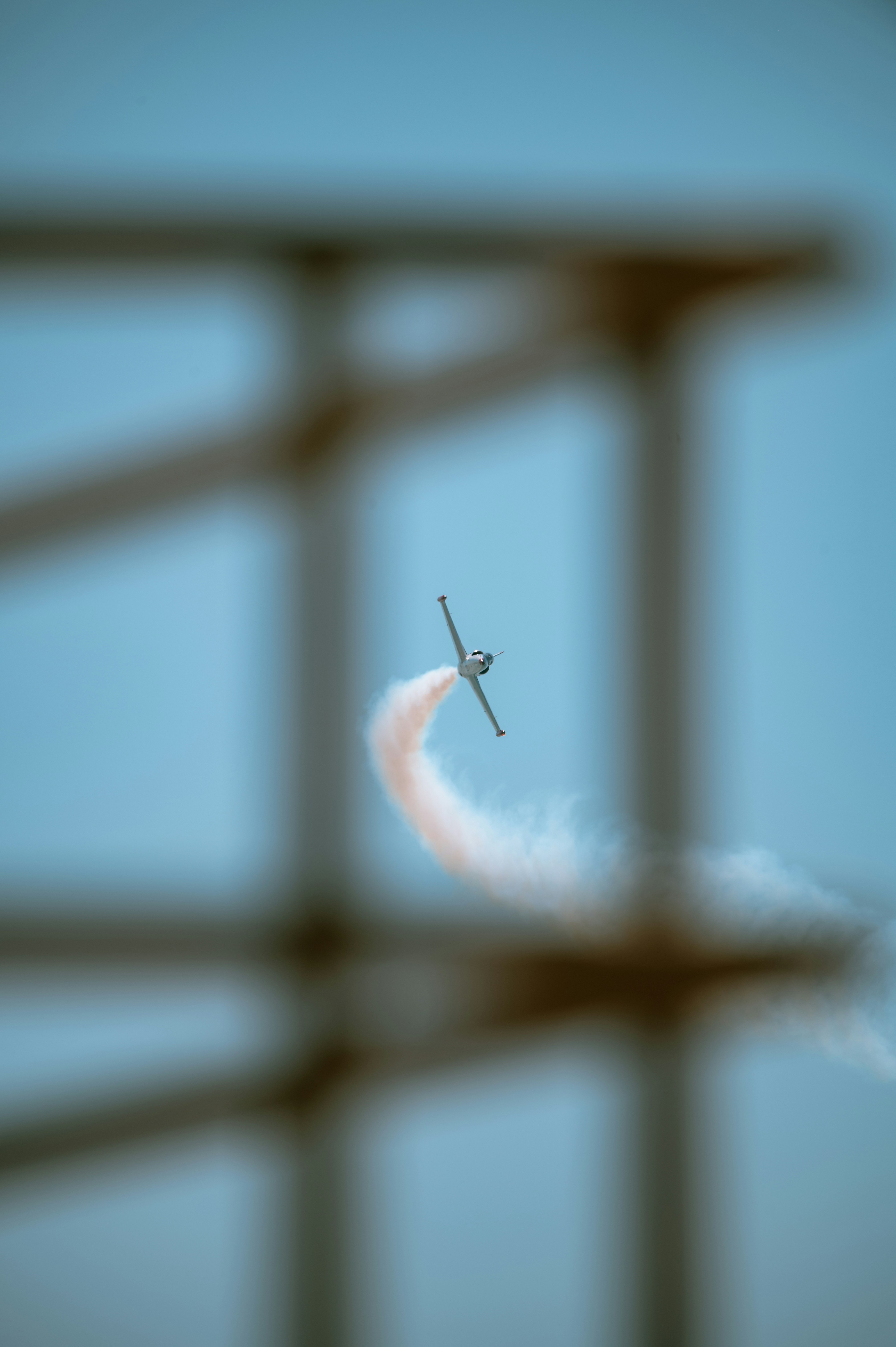 Smoke-Outlined Aerobatic Moment: A Tiny Plane Traverses Blue Sky Framed by Steel