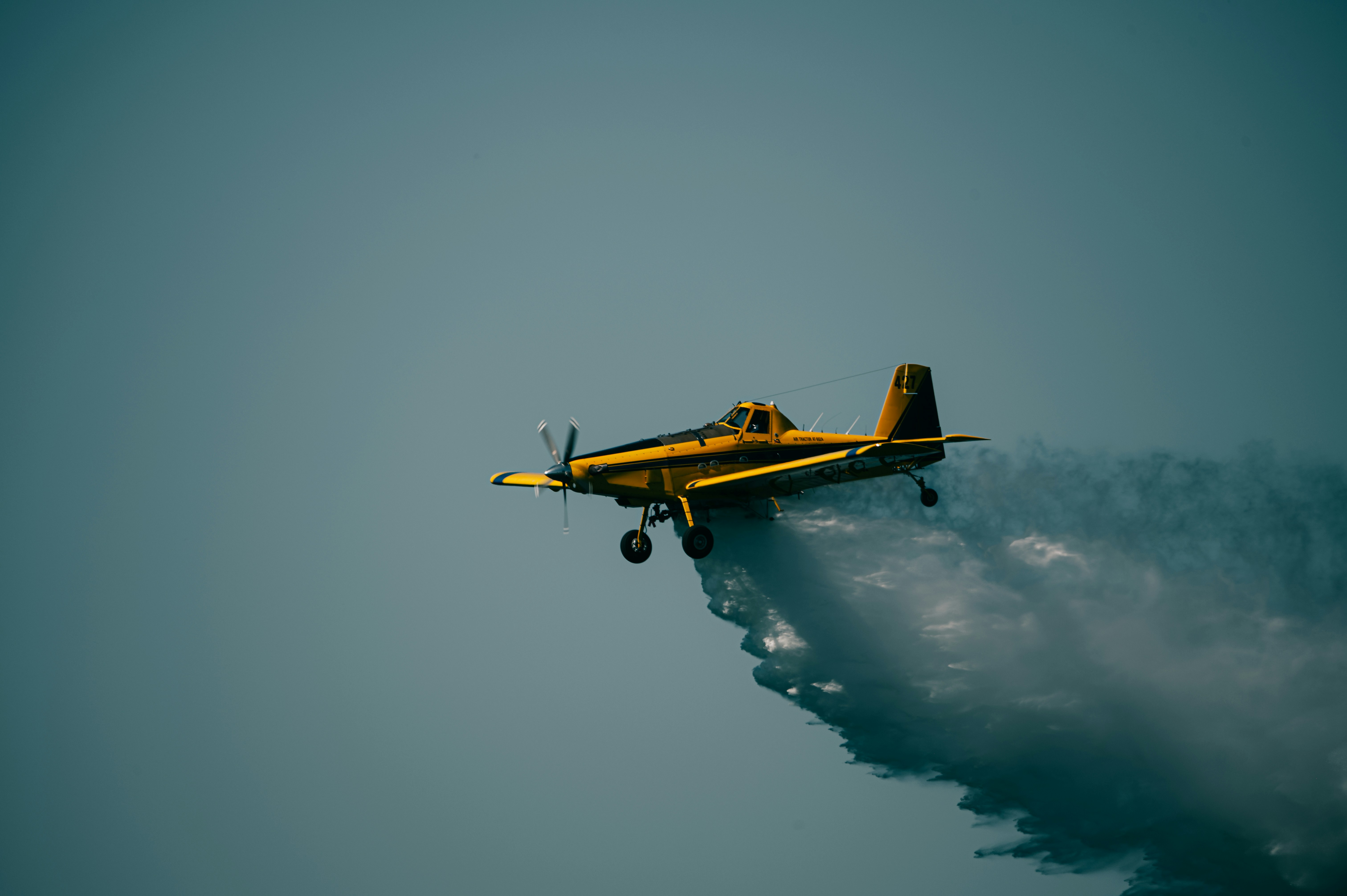 Yellow aerobatic plane carves a smoke trail across a pale blue sky