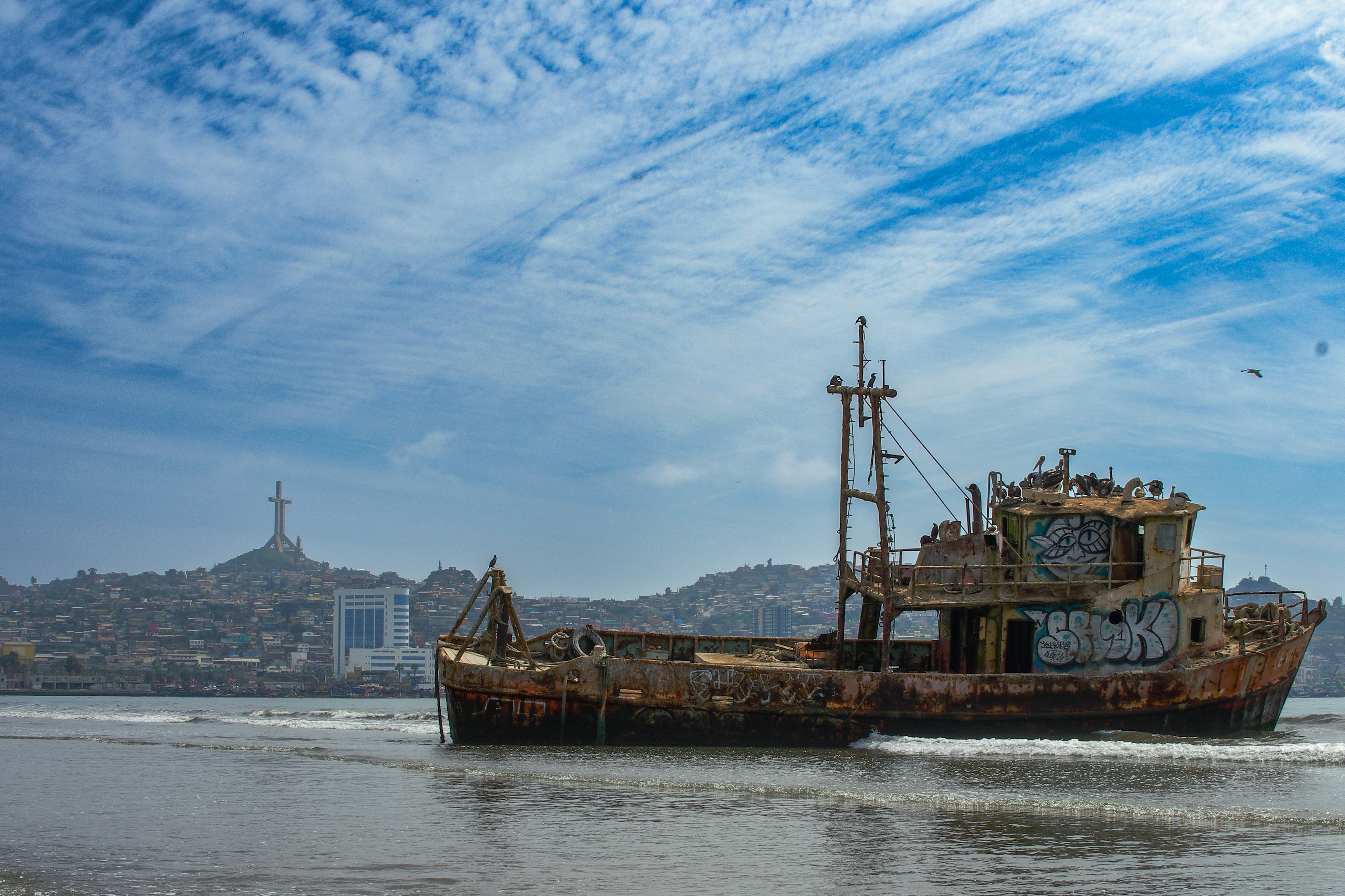 A weathered ship rests on calm waters under a sky filled with dramatic clouds.