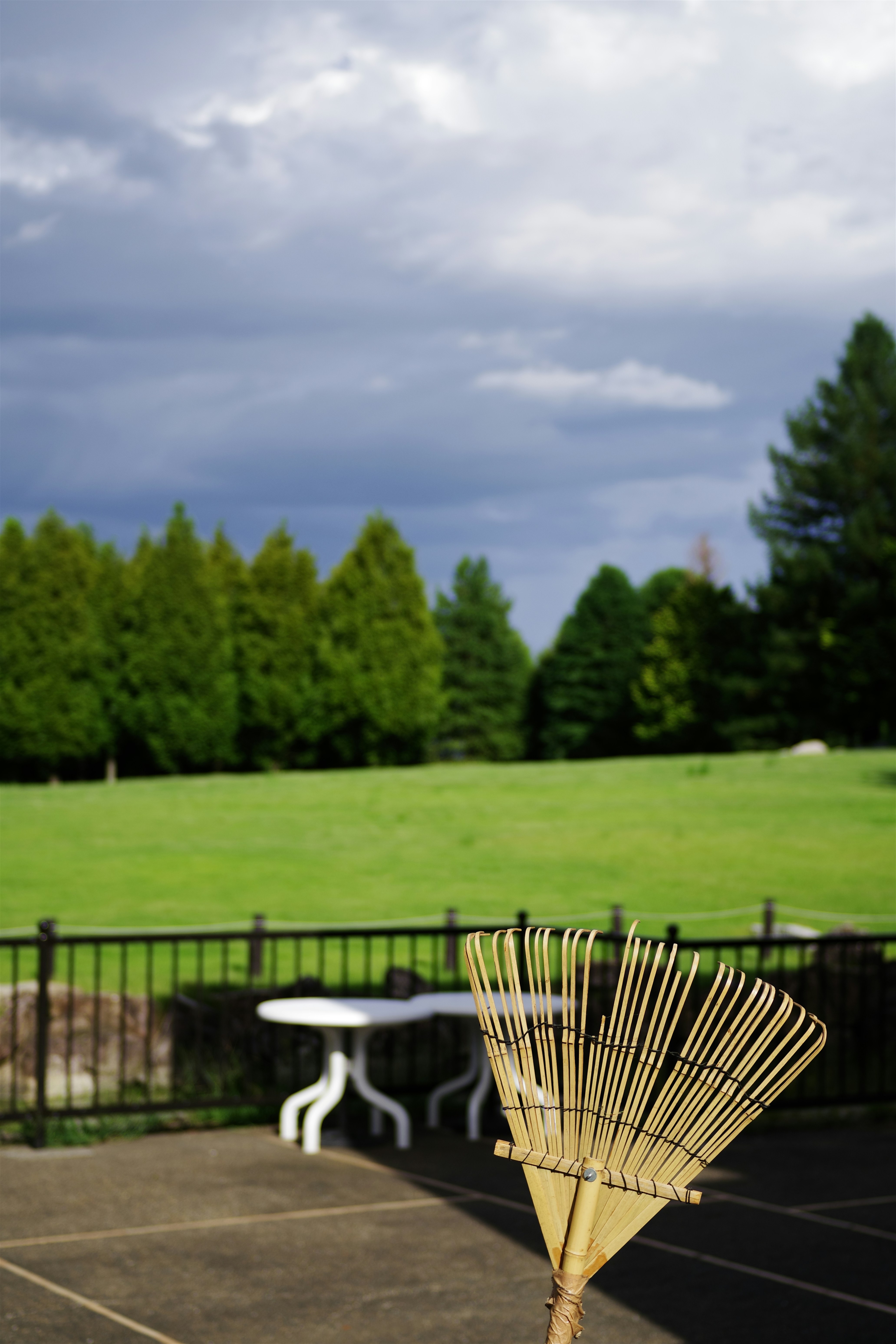 Bamboo rake dominates the foreground as a manicured lawn and distant trees stretch toward a moody, cloud-filled sky.