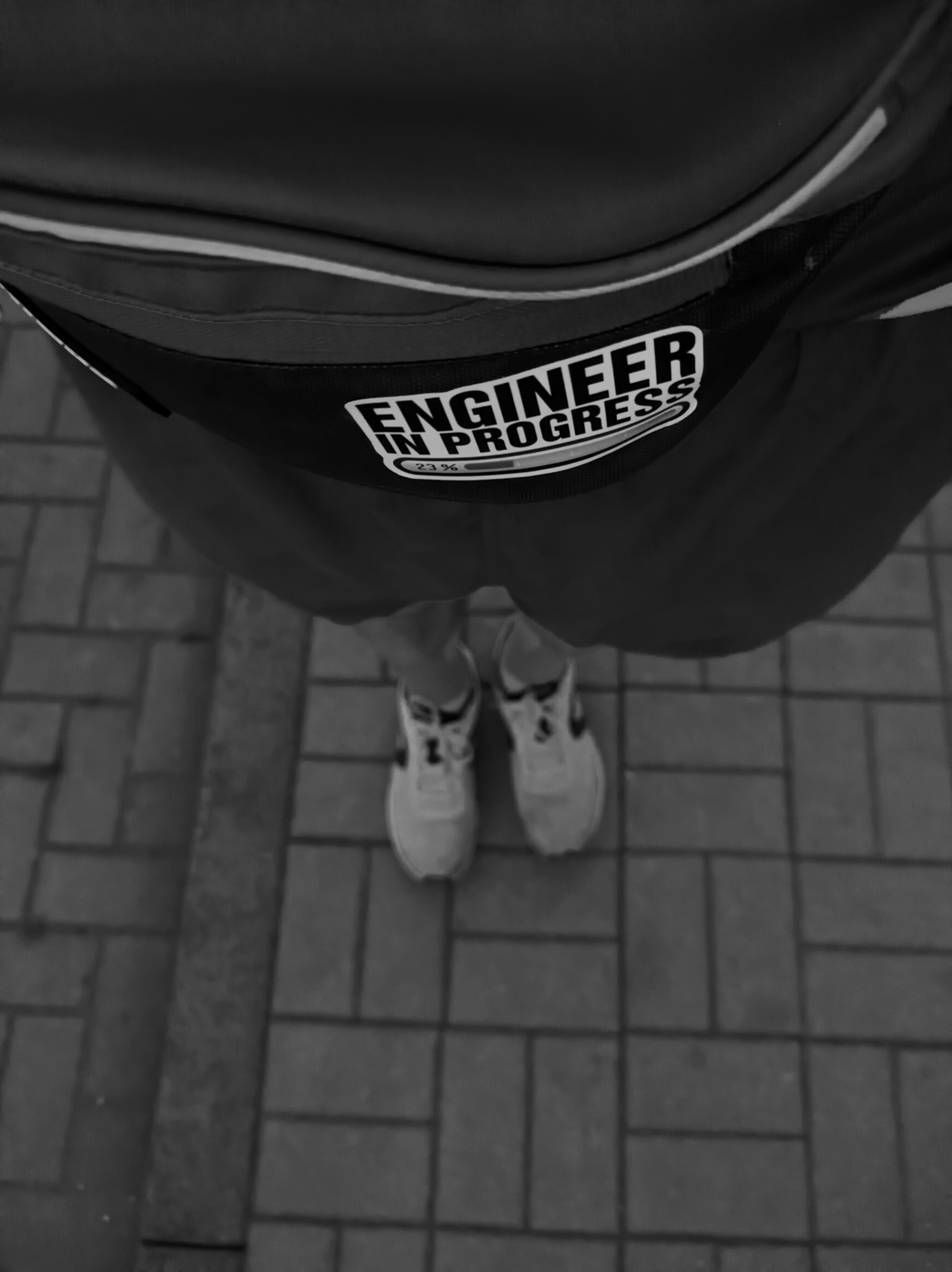 Top-down view of a jacket with a bold 'ENGINEER IN PROGRESS' logo patch, standing on a tiled pavement with sneakers visible.