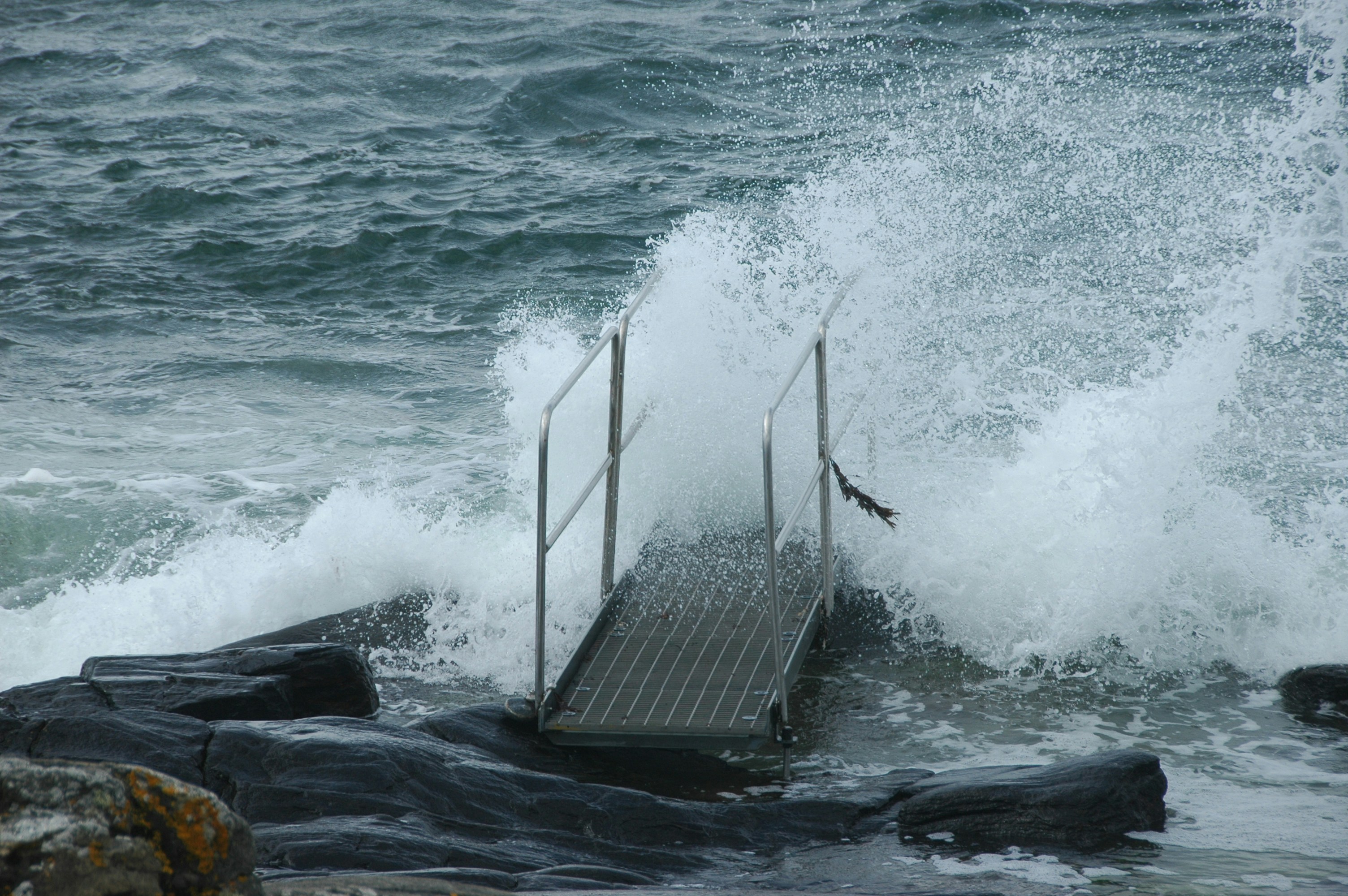 Rough Shore: A Wave Smashes Against a Metal Pier on Coastal Rocks