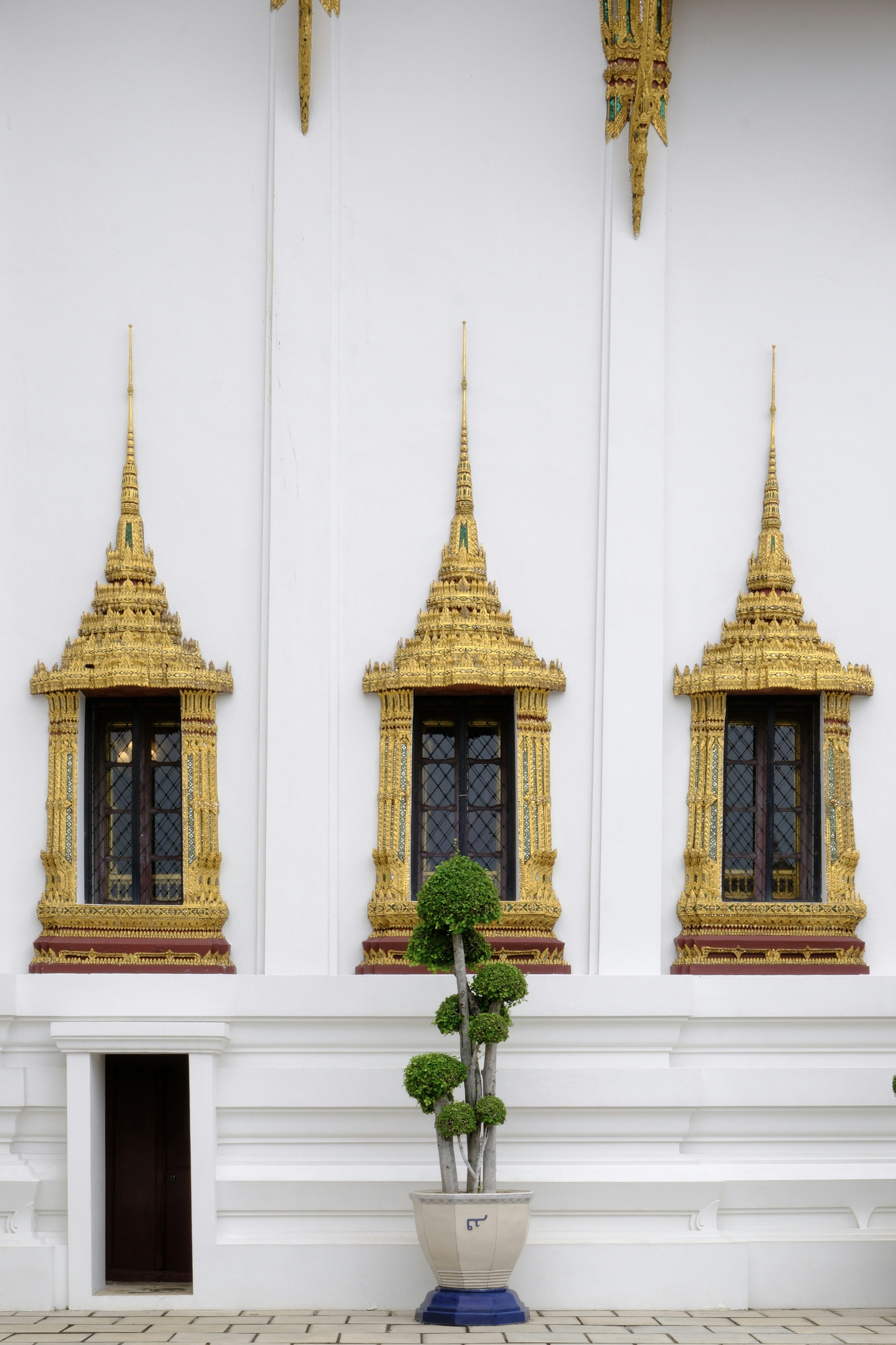 Three gilded temple windows flank a sculpted bonsai on a stark white wall