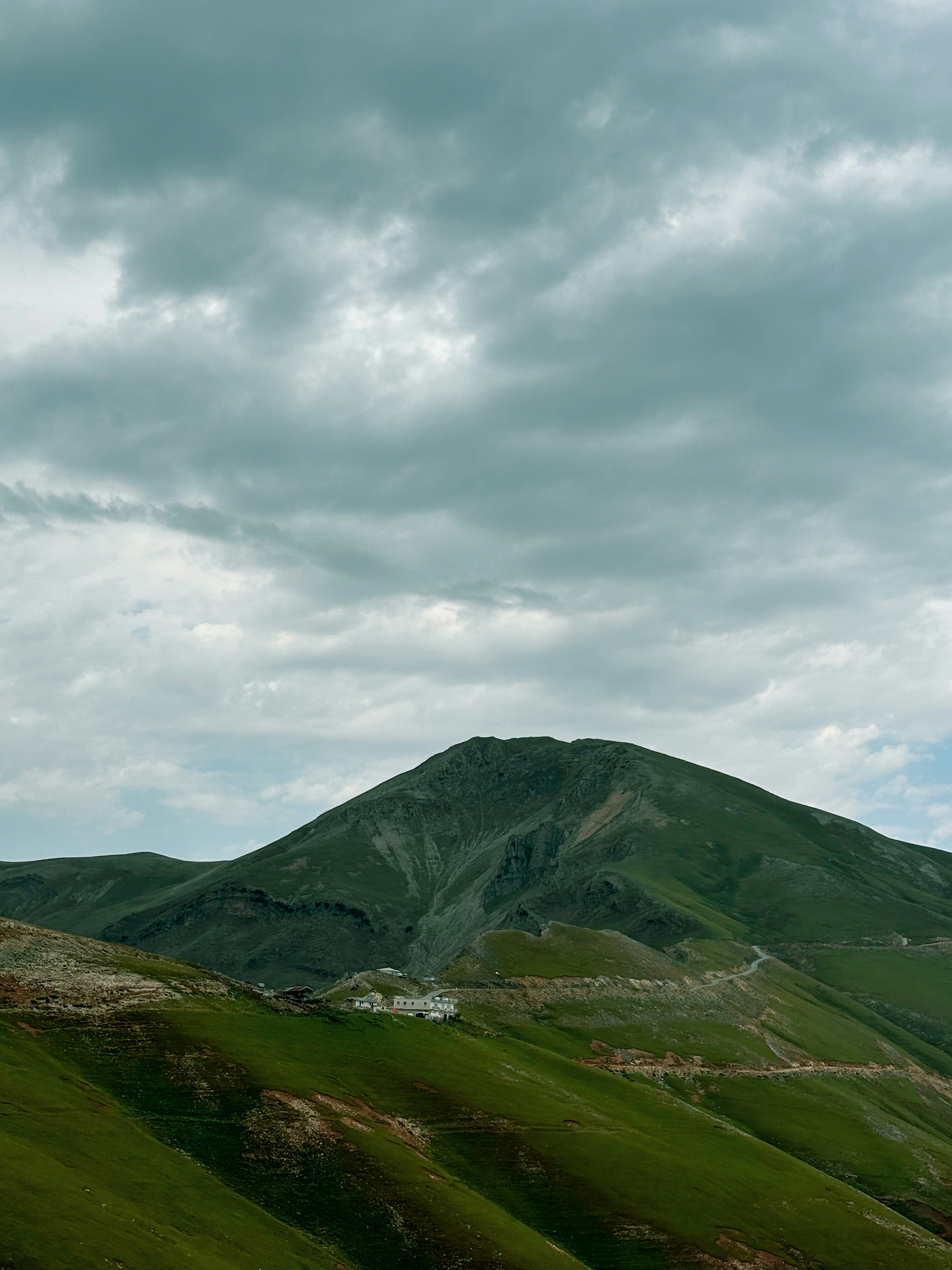 Rolling green hills with a solitary white cottage beneath a moody, cloud-filled sky.