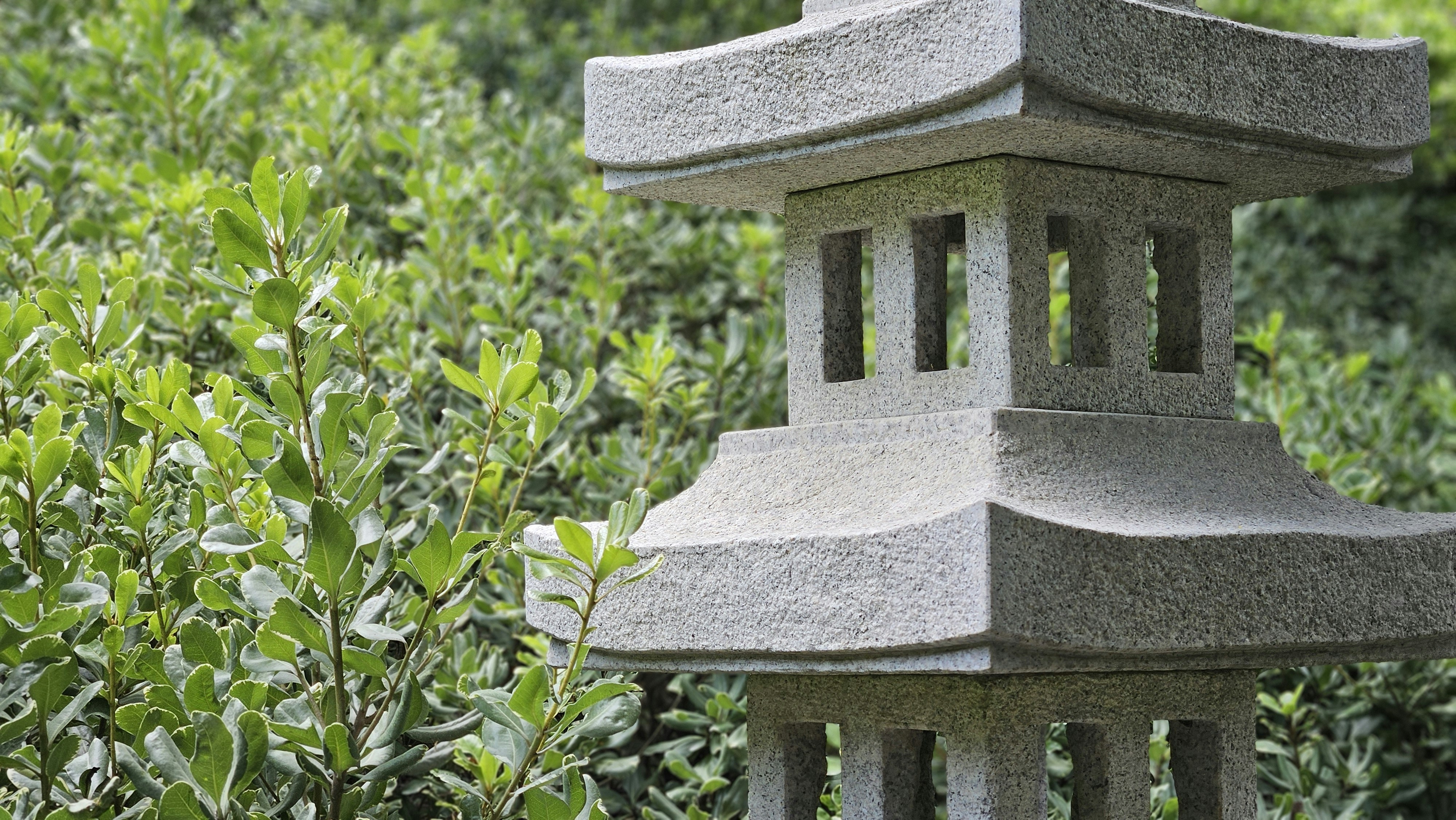 Stone lantern rises beside lush greenery in a tranquil garden, highlighting traditional stone architecture.