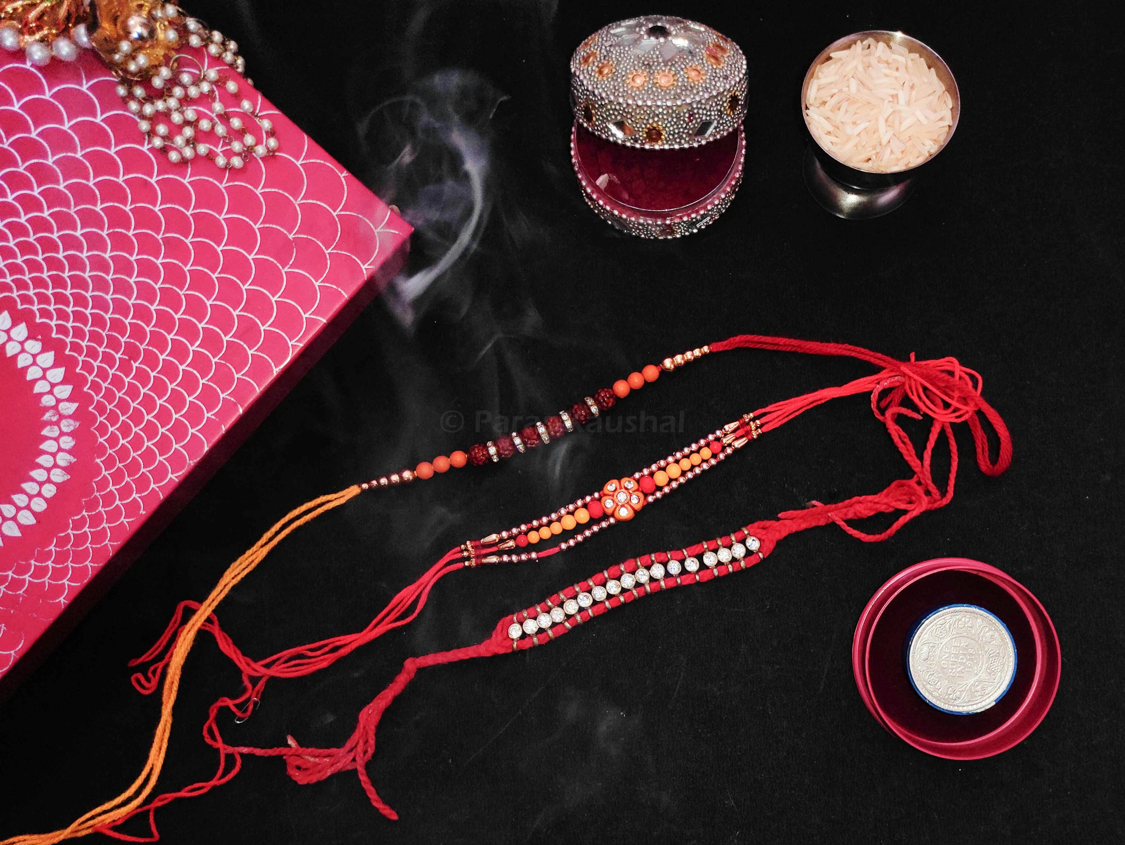 Bead-embroidered cords stretch across a dark surface, framed by a pink patterned gift pouch and small containers, highlighting color and texture of the strands.