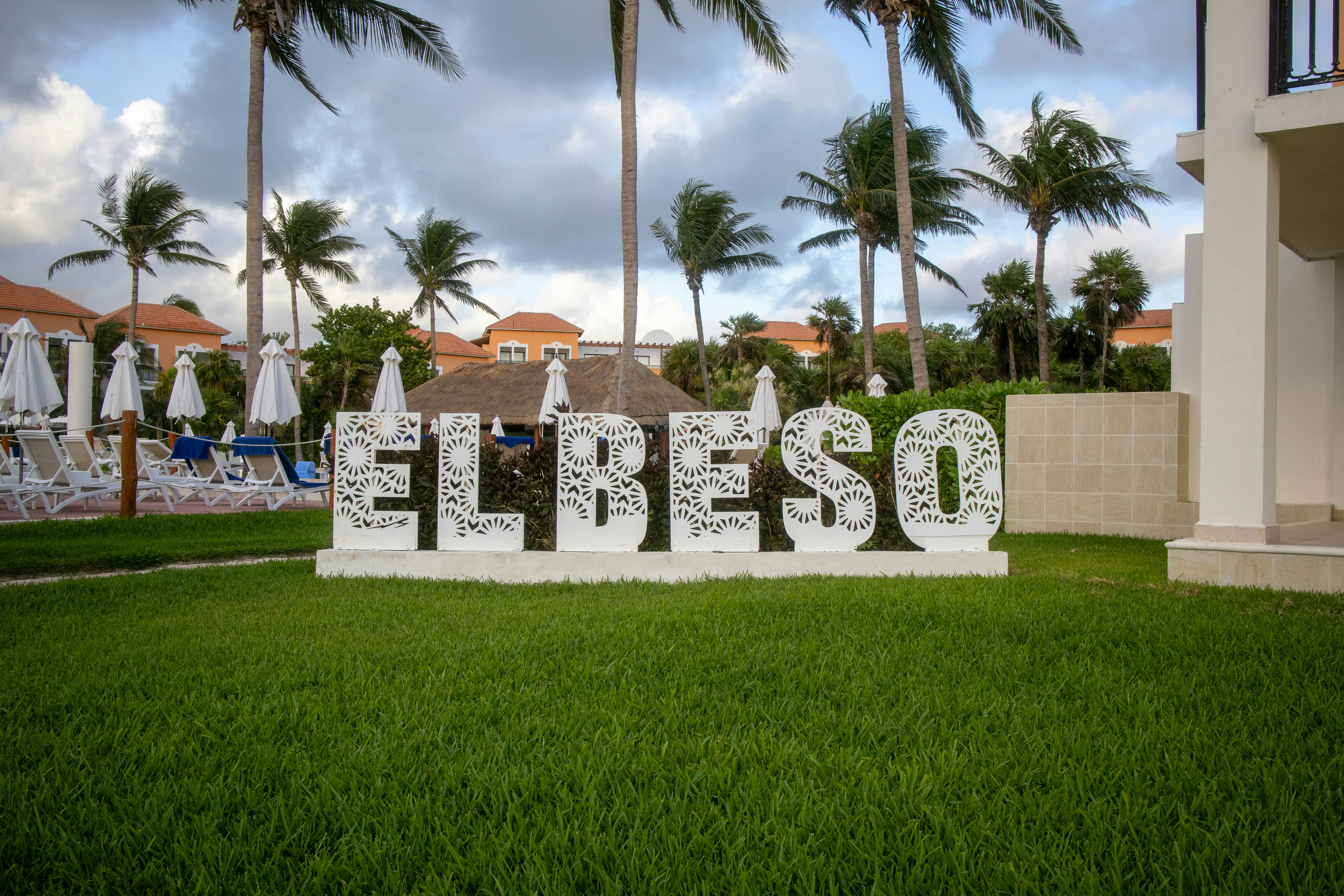 EL BESO: Large Decorative Letters Anchoring a Palm-Shaded Resort Lawn