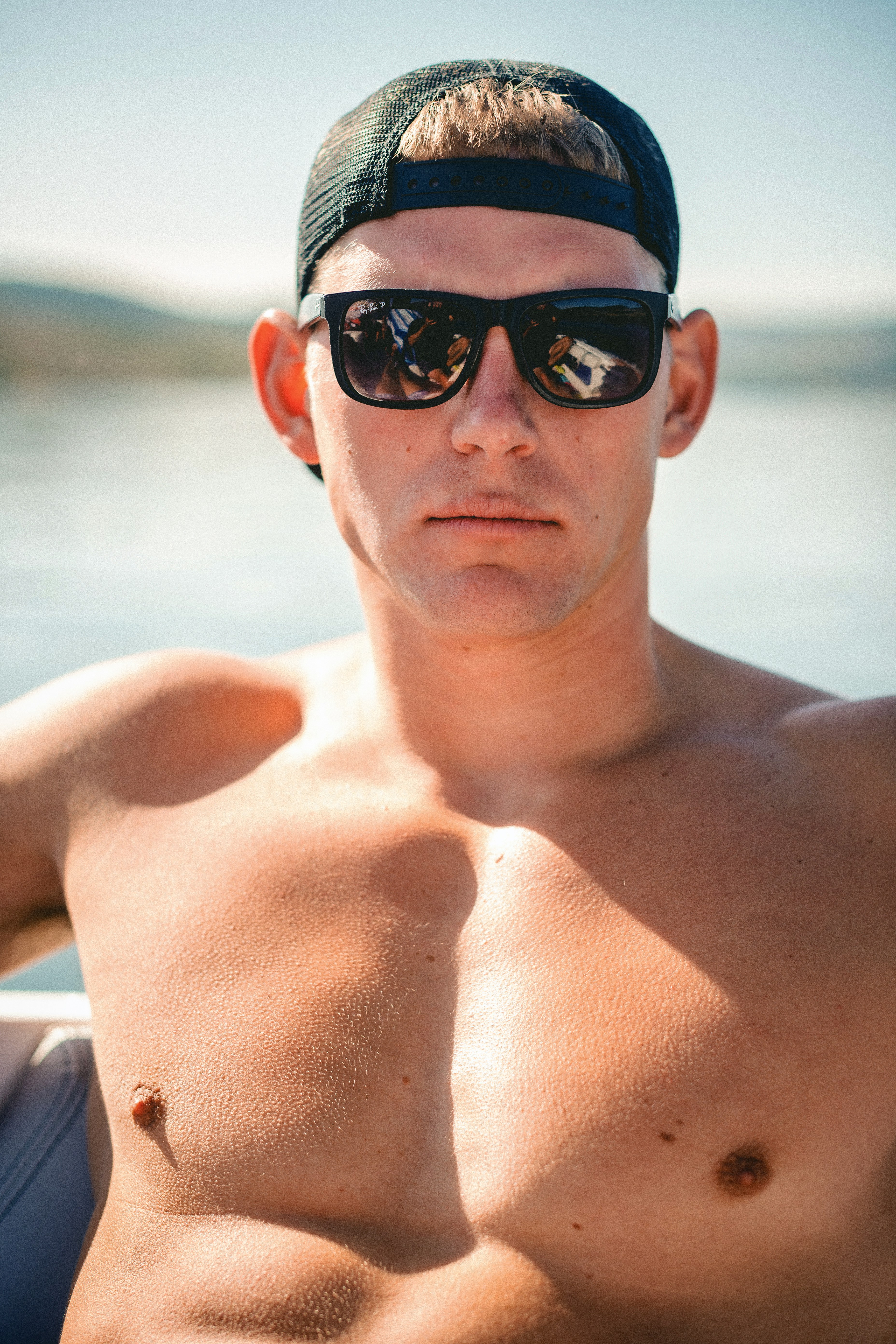 Man with sunglasses and cap relaxing on a boat under bright sunlight.