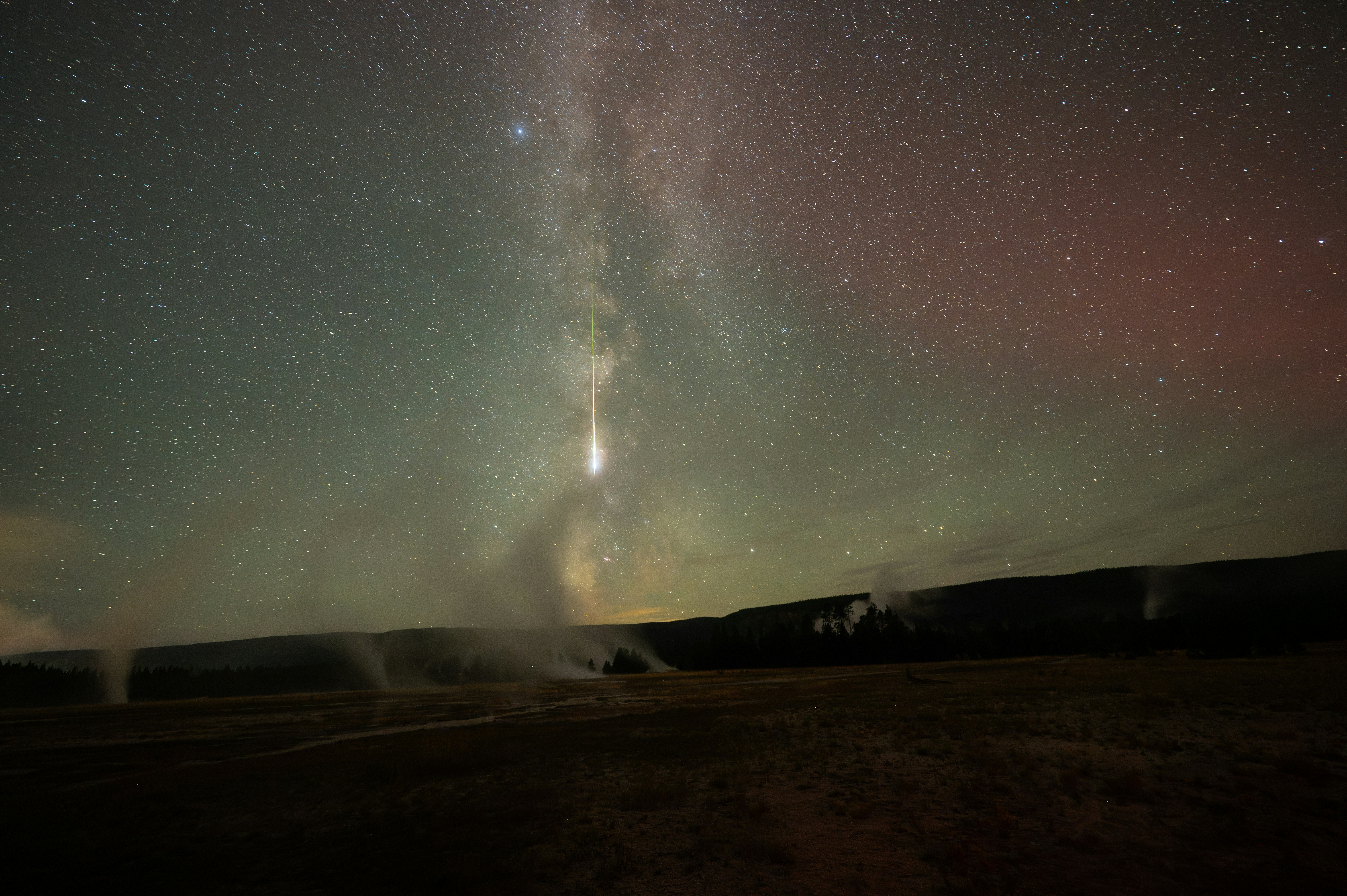 Meteor streaks through star-filled sky above Yellowstone geysers.