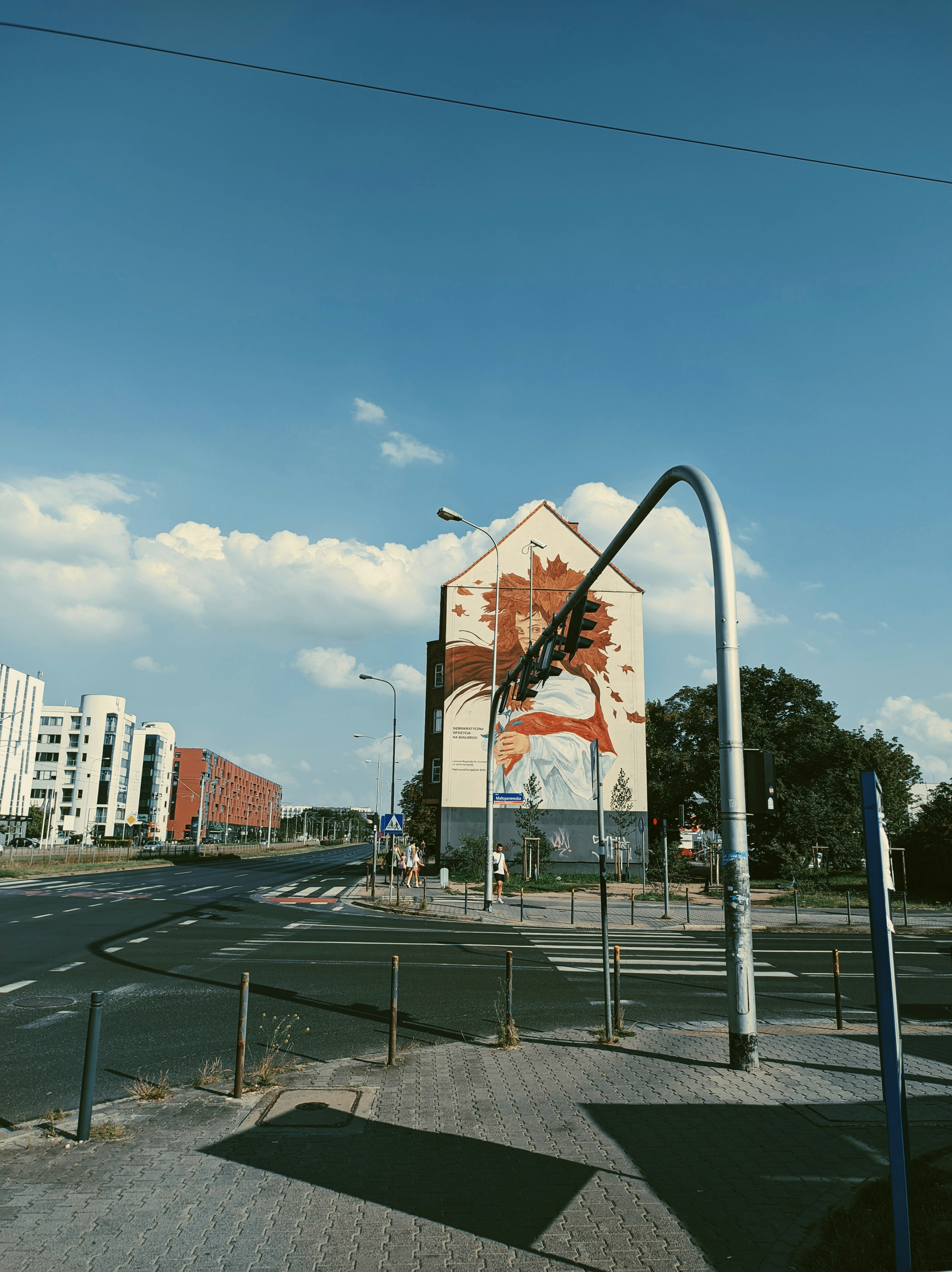A vibrant mural painting adorns a tall building along a city street, with a looping metal arch in the foreground under a clear blue sky.
