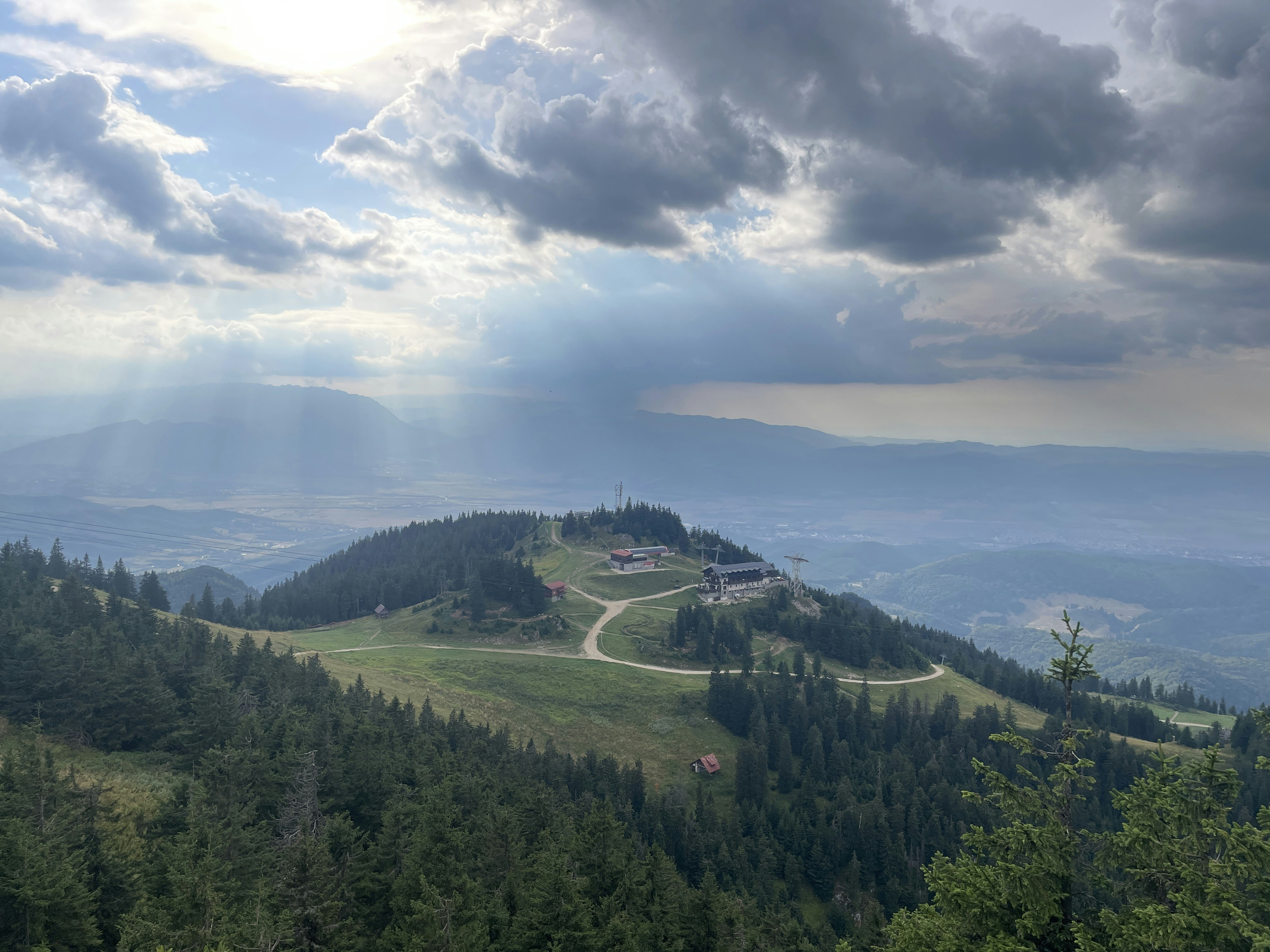 Sunlight pierces through cloud cover, casting radiant beams over a lush mountain landscape.