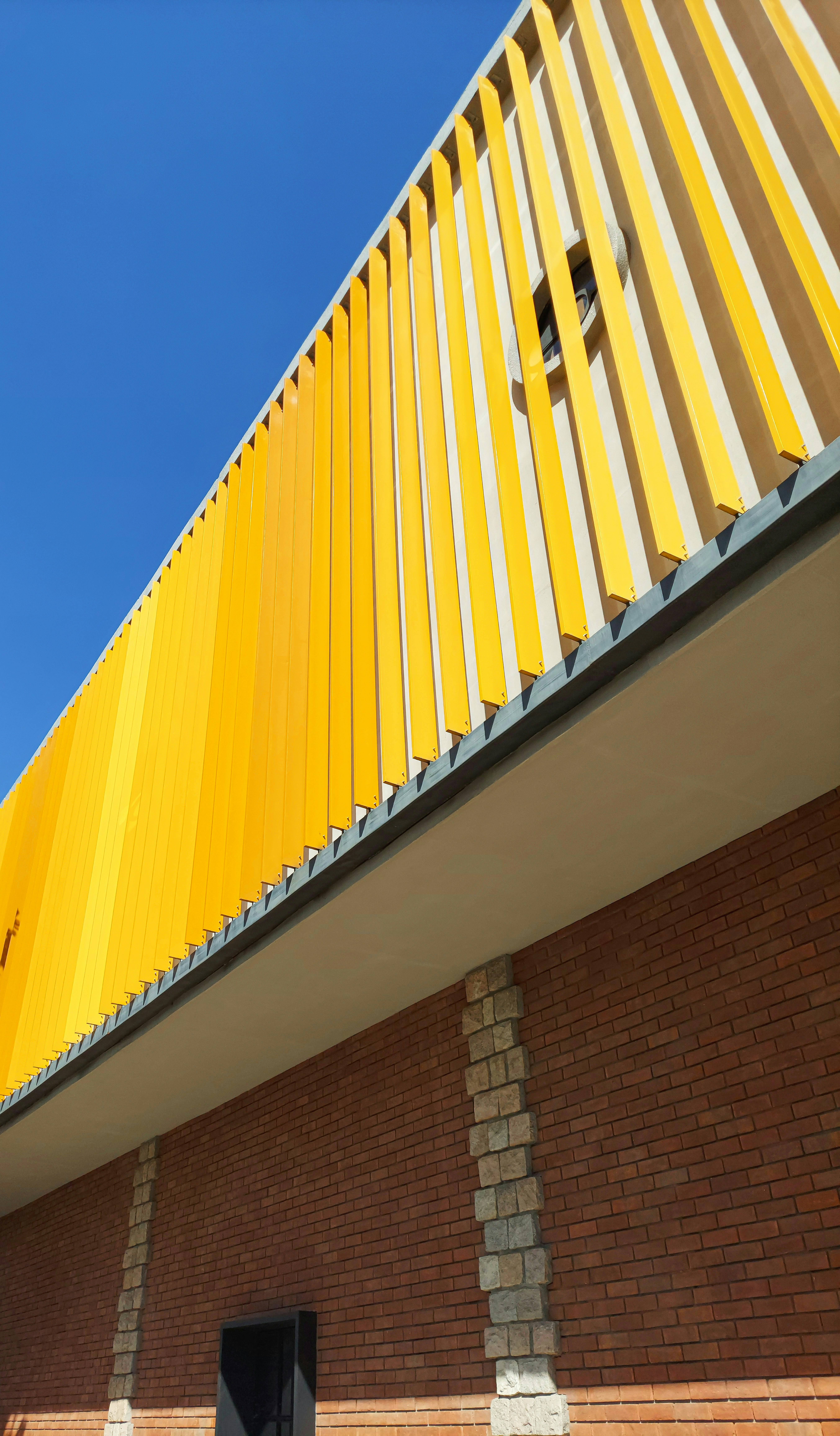 Vivid yellow vertical slats run along a diagonal railing above a brick facade against a clear blue sky.