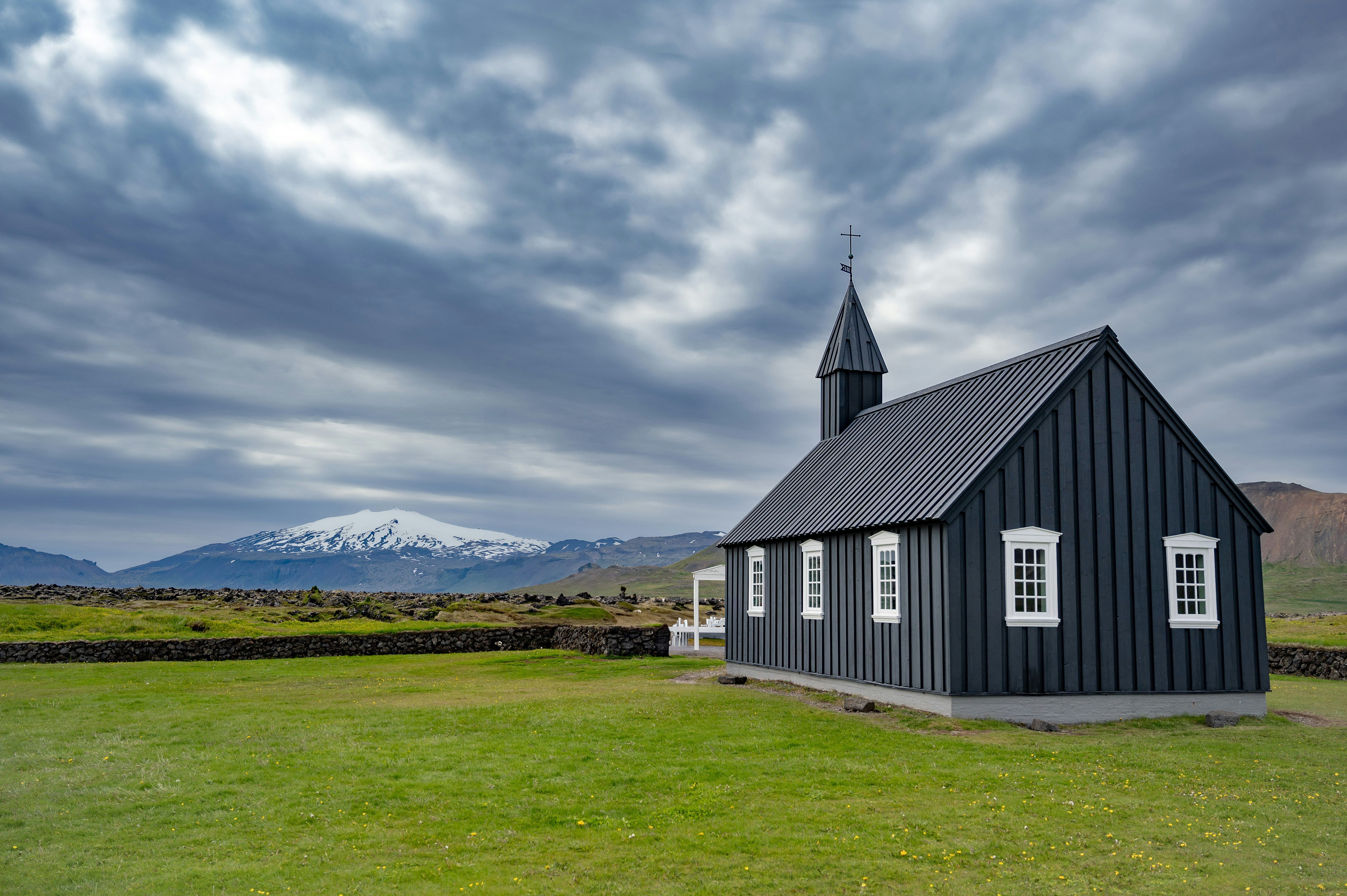 A small black church with a steeple on a cloudy day