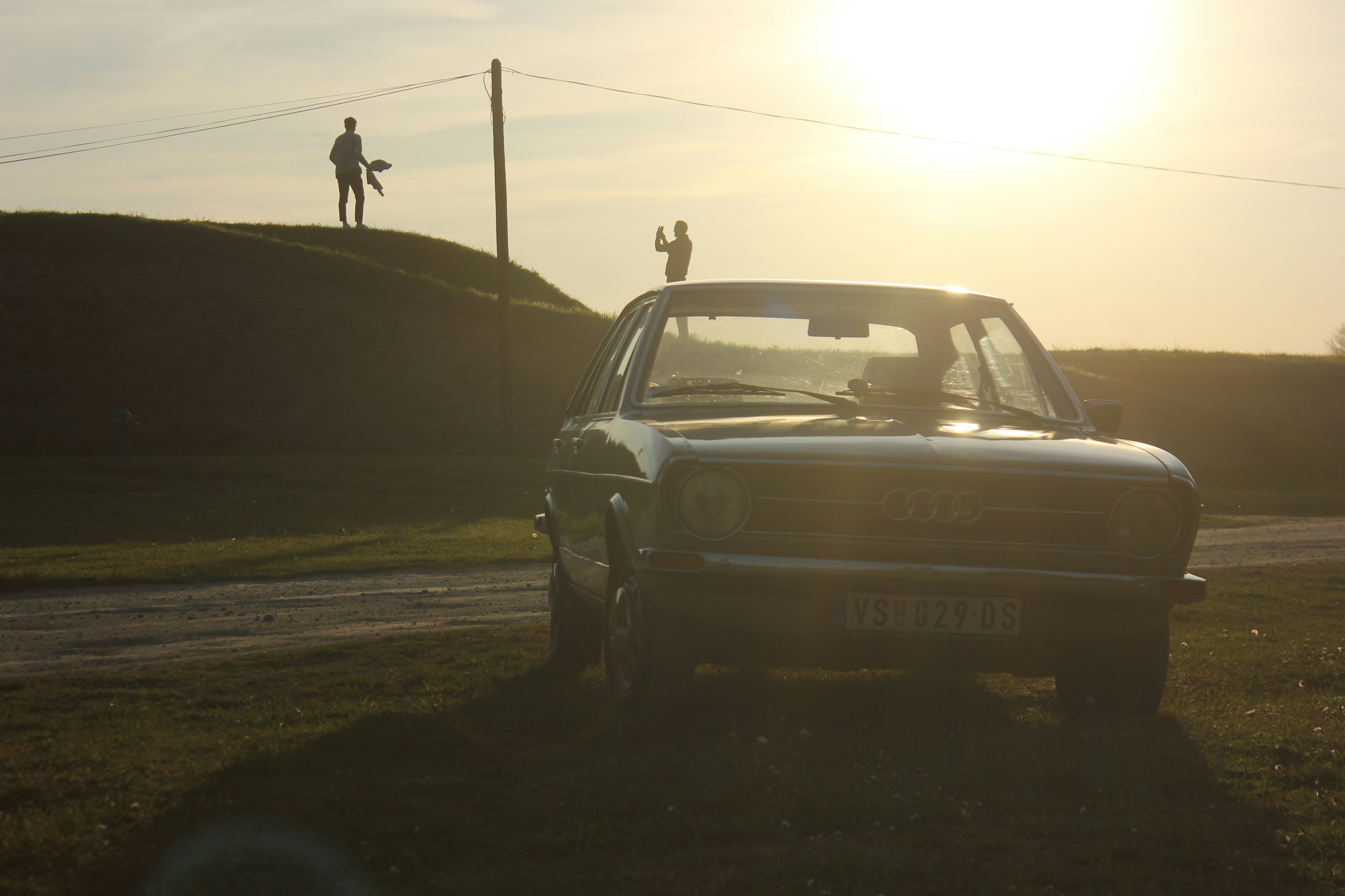 Amber Hour Overlook: A Vintage Sedan and Distant Silhouettes on a Crest