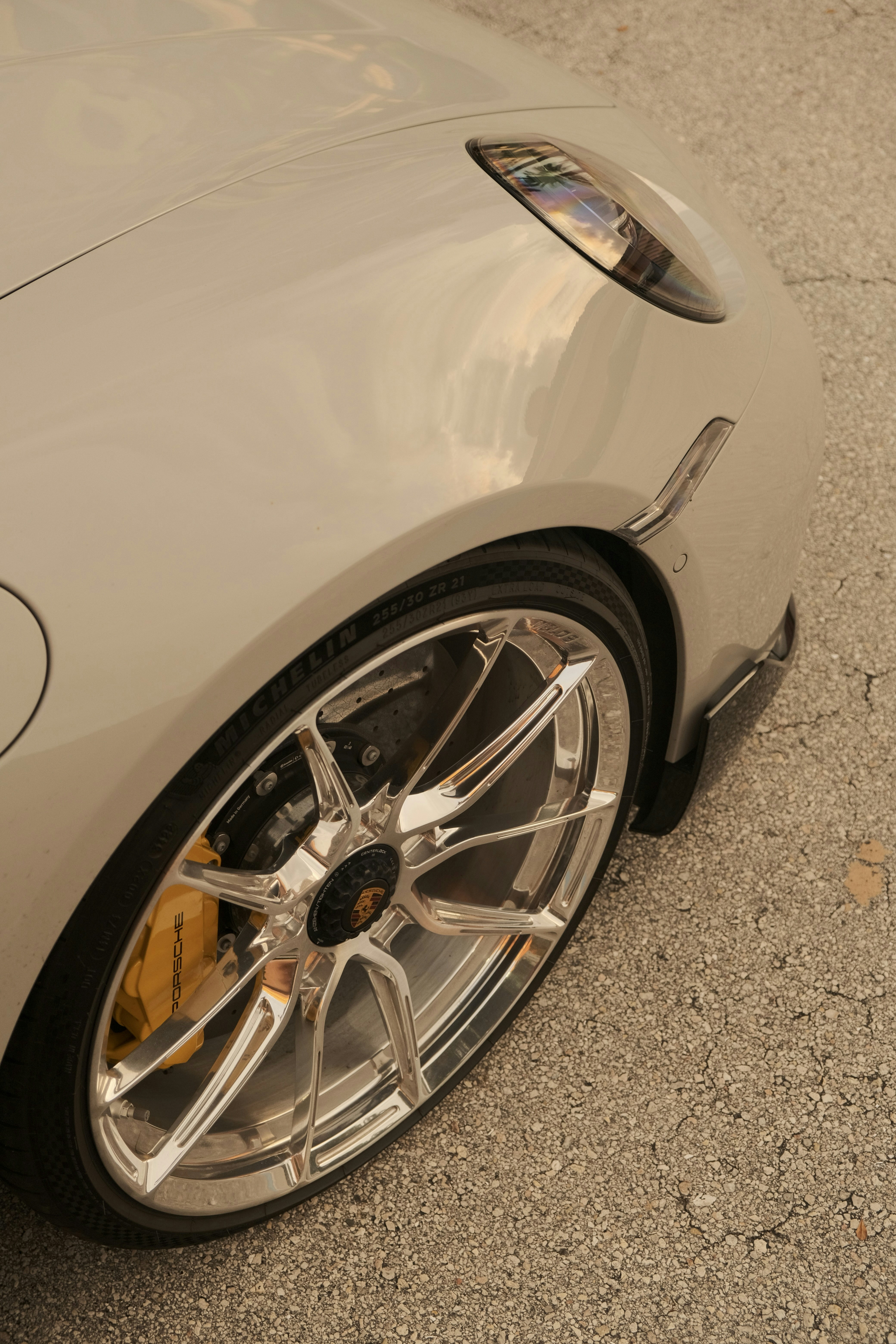 Chrome-spoked Porsche wheel with gold brake caliper under soft light