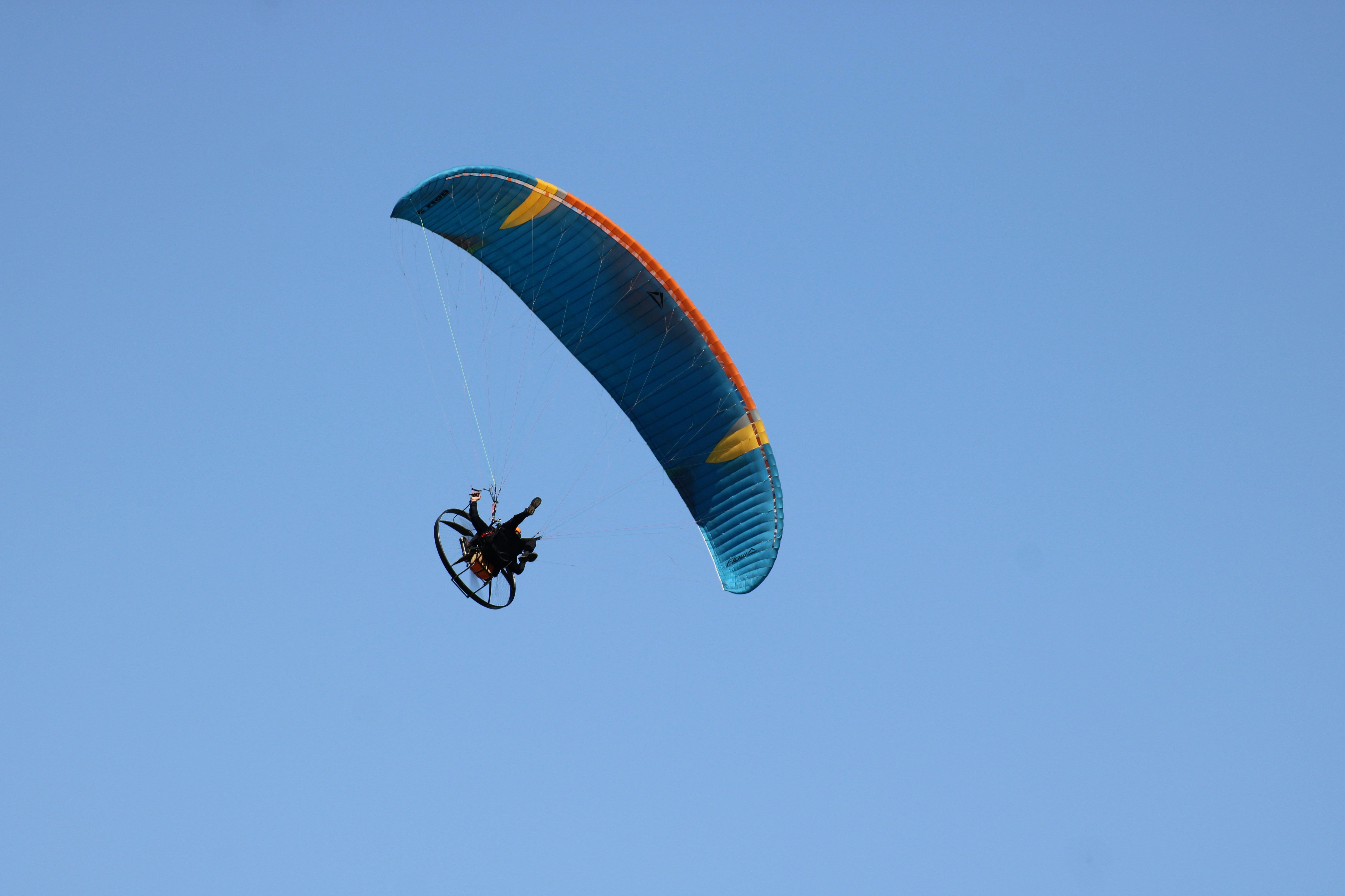 Sapphire Glide: a lone paraglider etching a curved arc across a clear sky