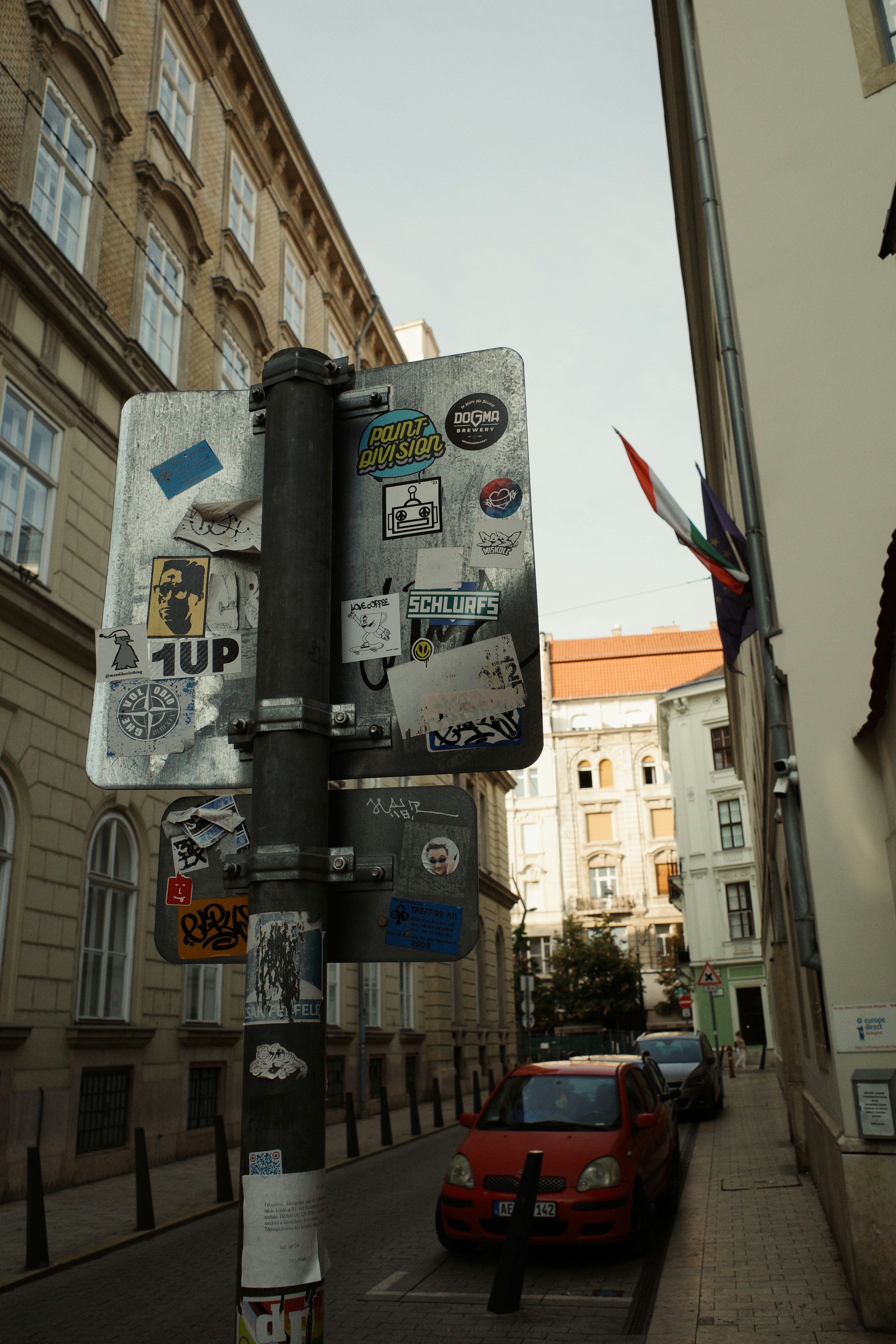 Sticker-Laden Signpost Framing a Quiet European Street