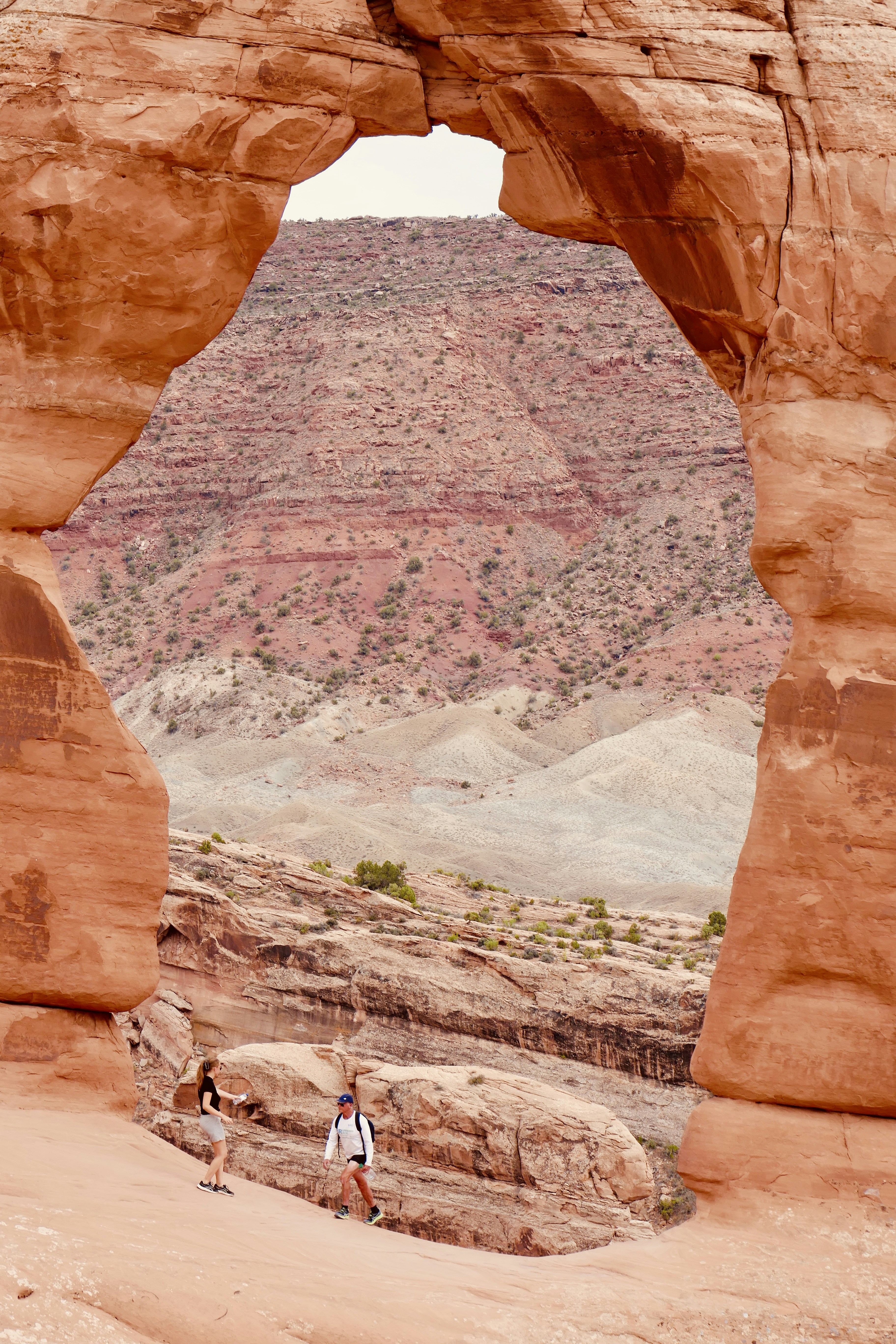 A person standing in front of a large rock arch photo – Free Arches ...