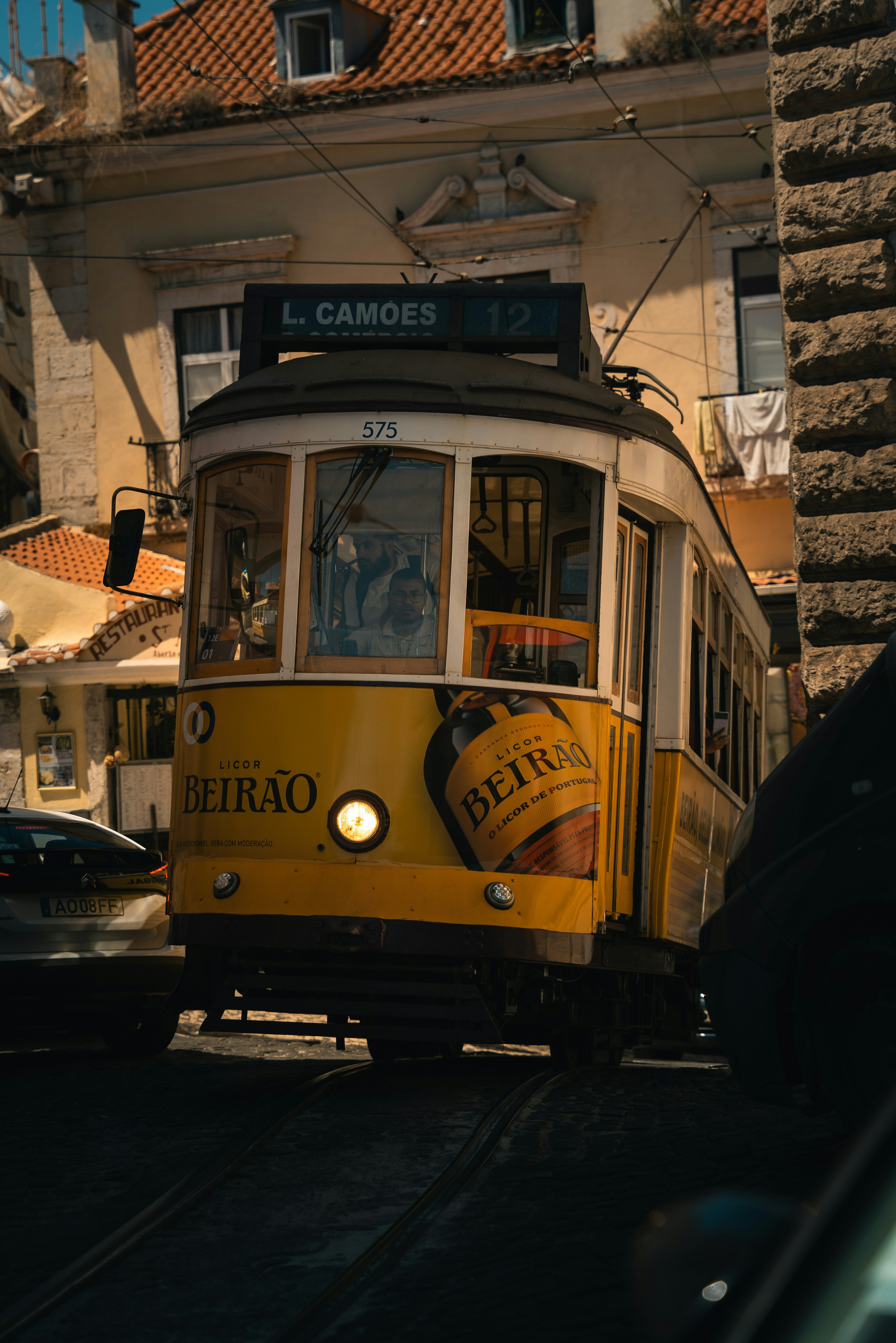 A sunlit yellow tram threads a cobbled Lisbon lane